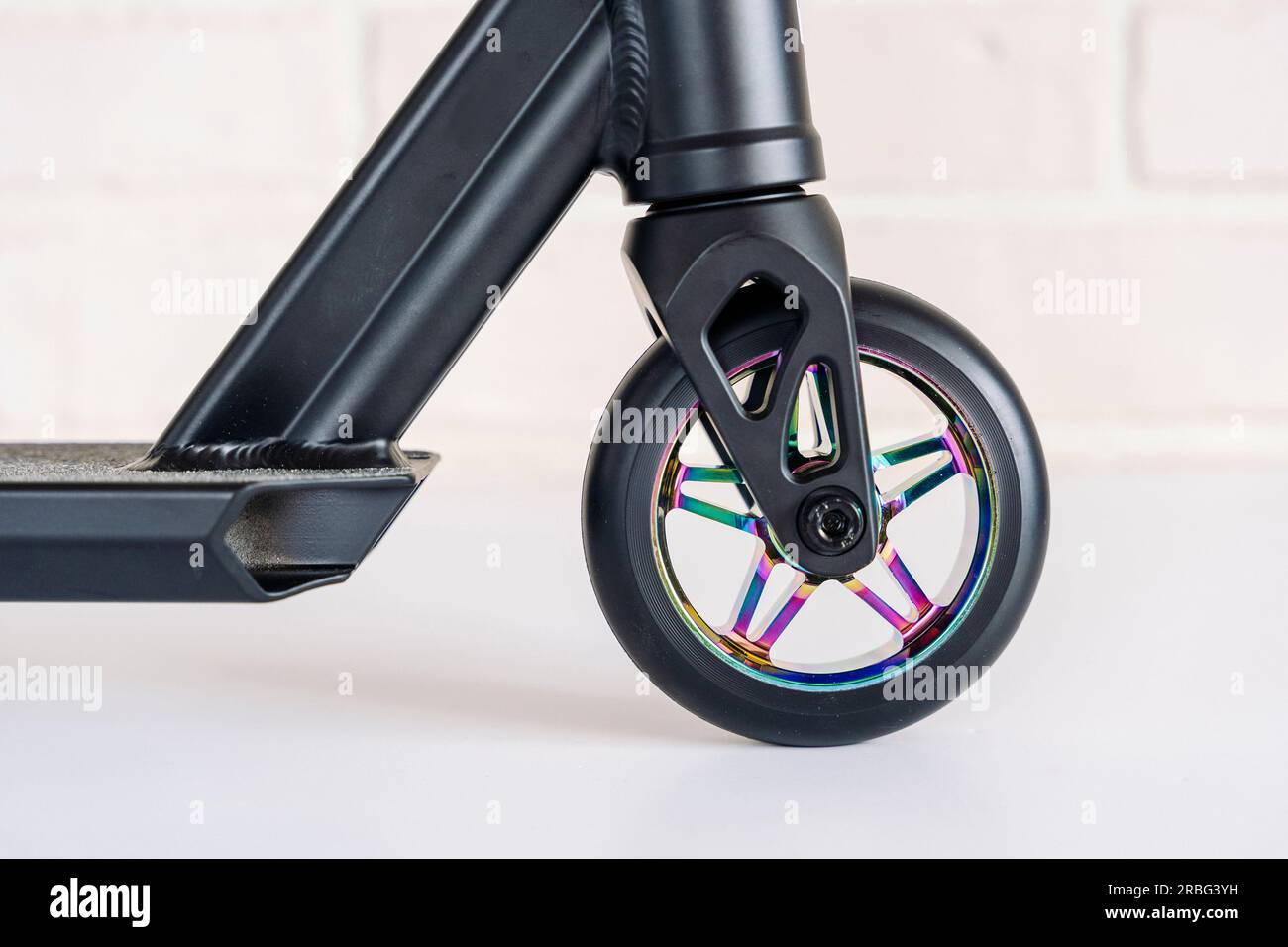 The front wheel of a rainbow-colored stunt scooter against a light ...