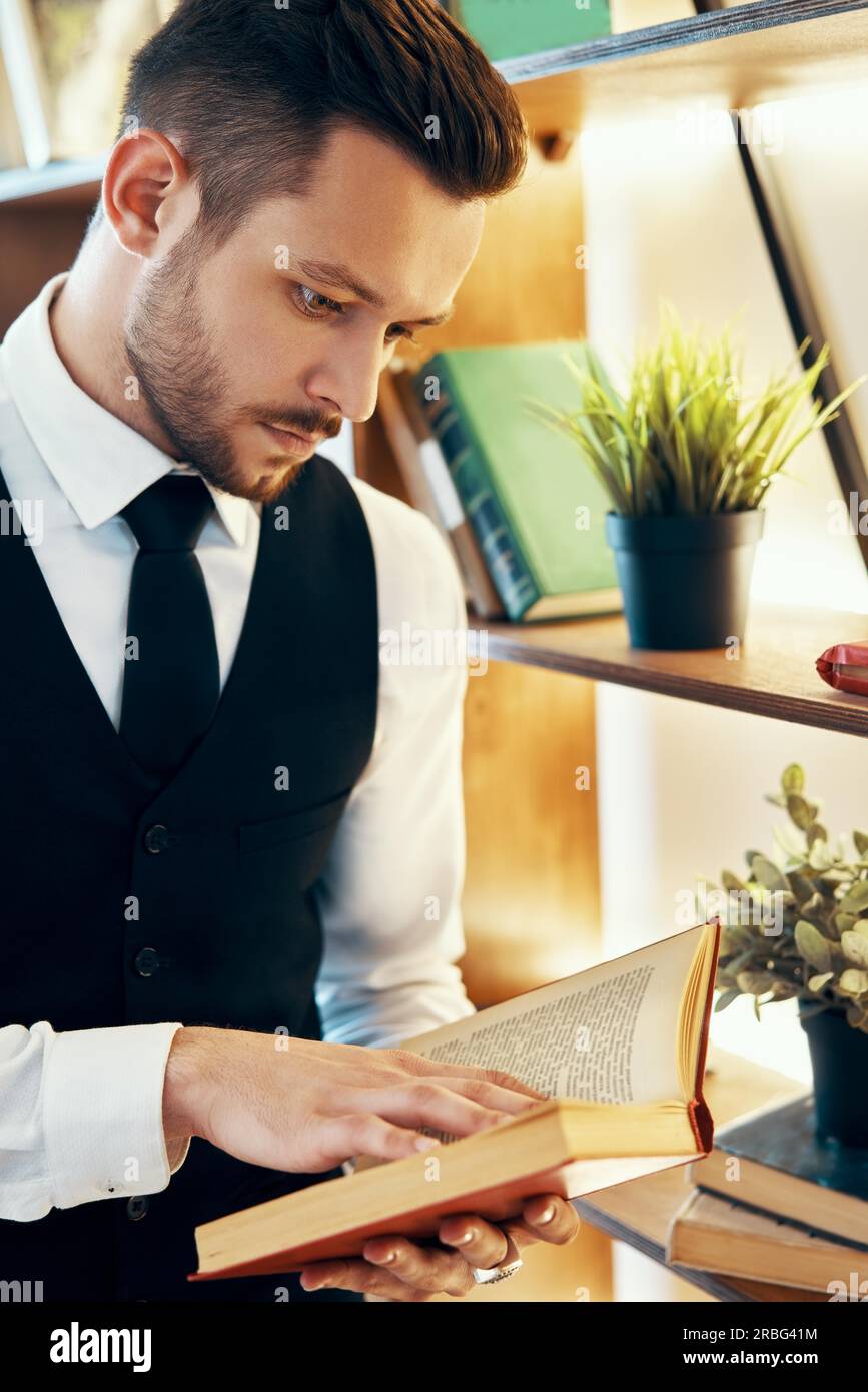 Handsome young man in elegant suit reading a book in modern luxury ...