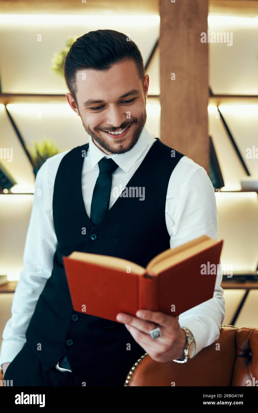Handsome young man in elegant suit reading a book in modern luxury ...