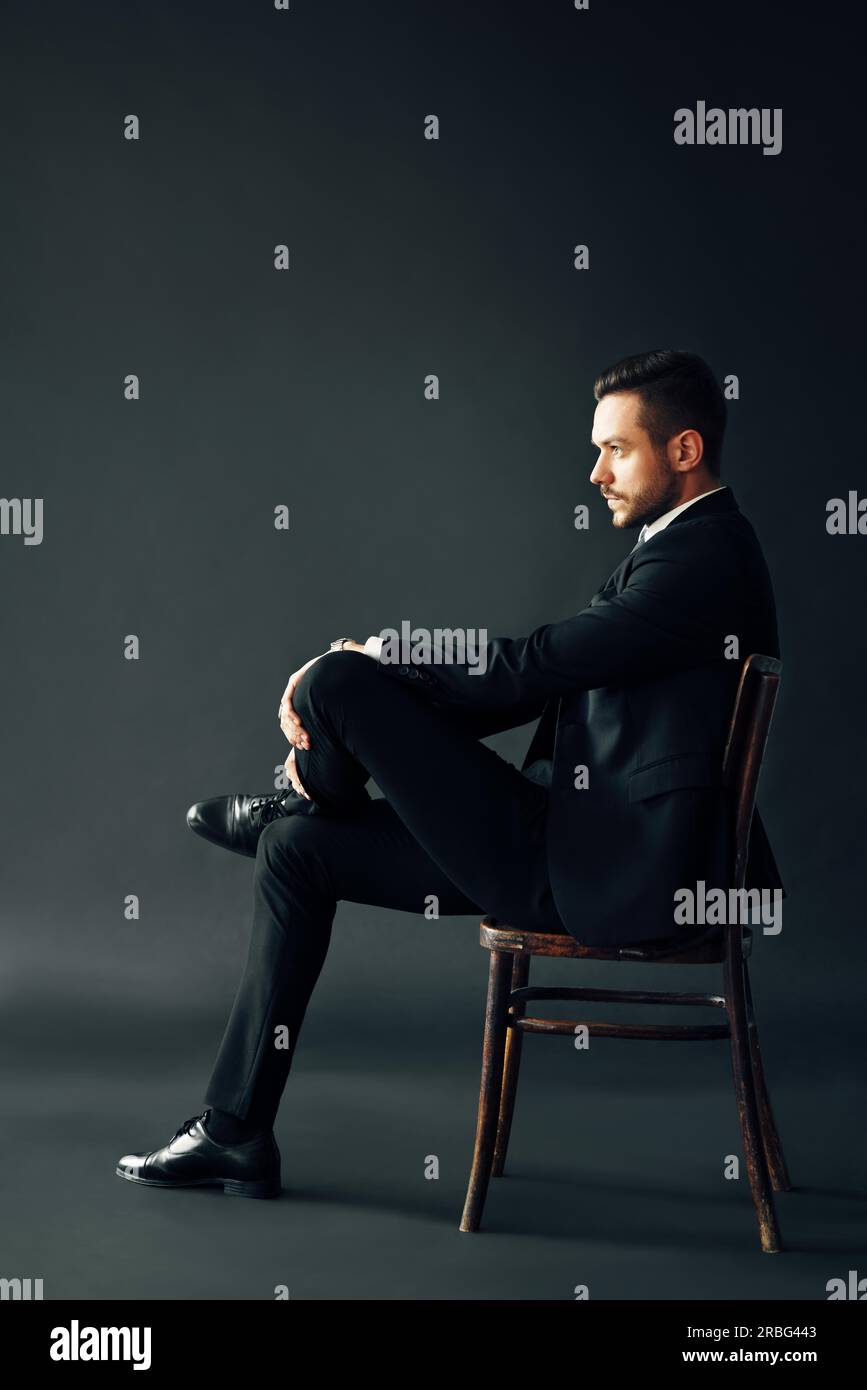 Confident handsome man in black suit sitting on the chair on dark ...