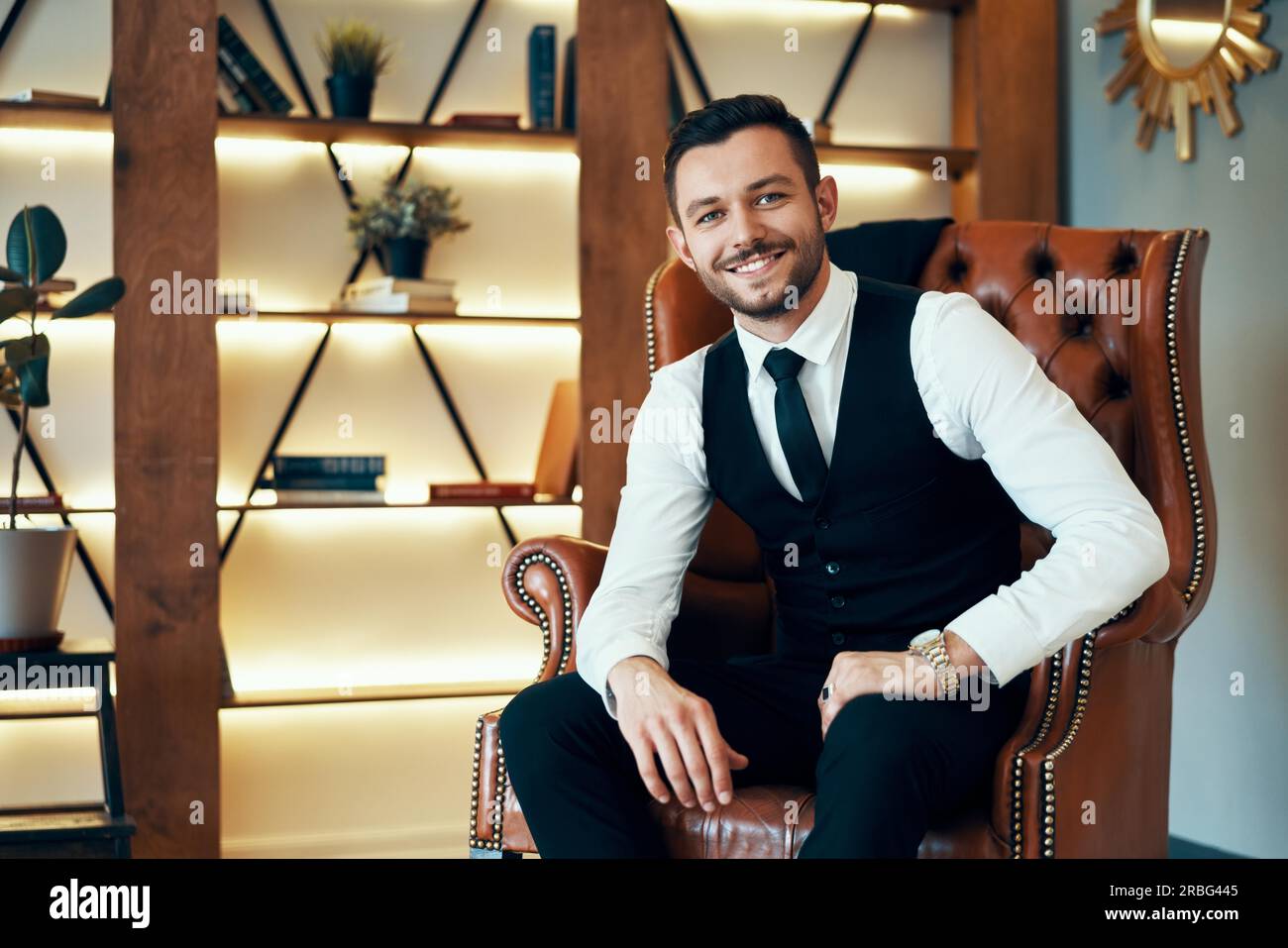 Smiling handsome man sitting and posing in armchair in modern luxury ...