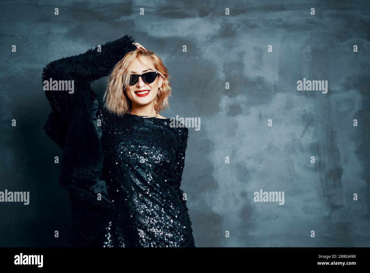 Pretty blonde woman in little black dress posing on grey background ...