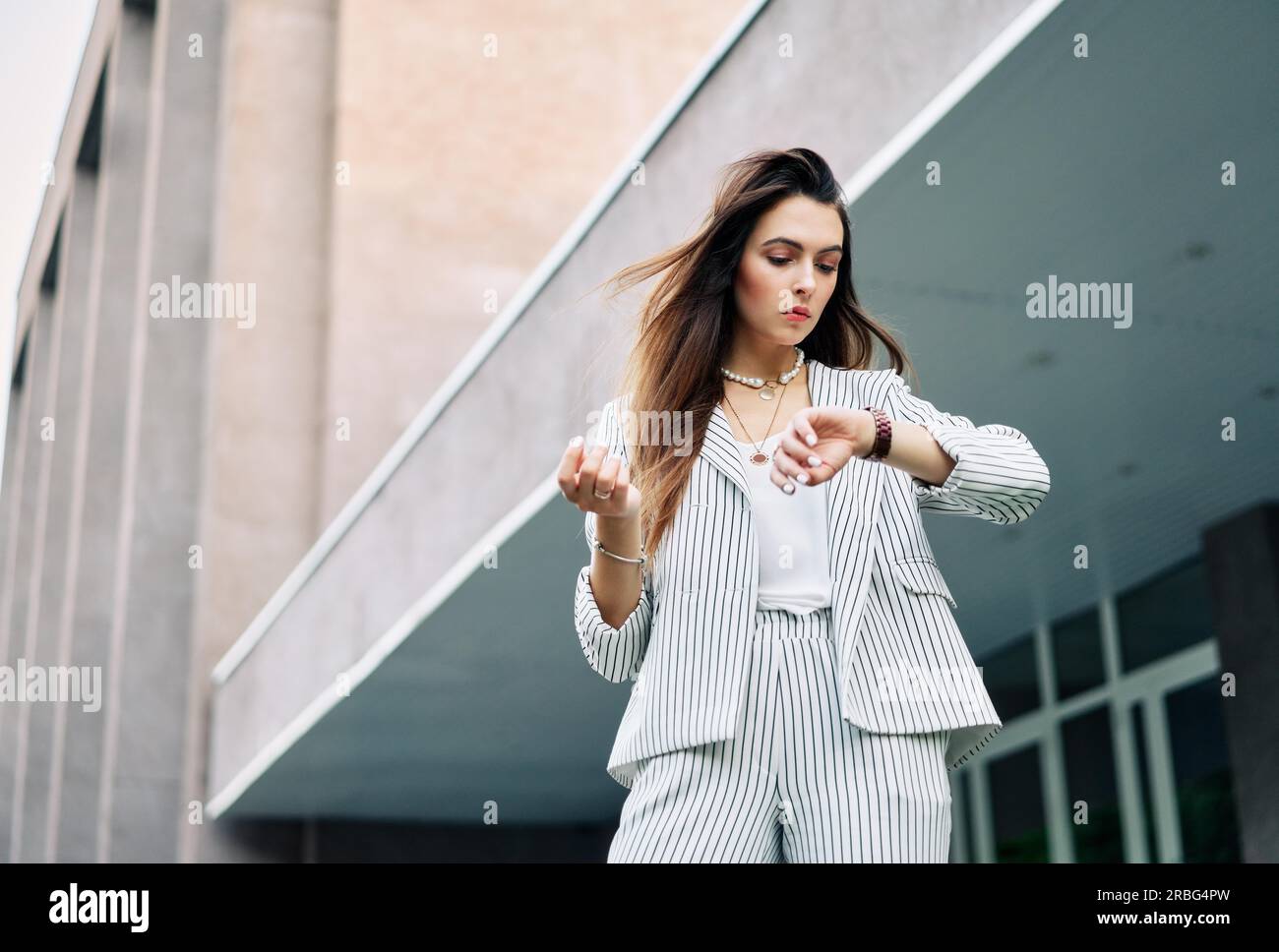 Stylish young business woman look her watch on city street background ...