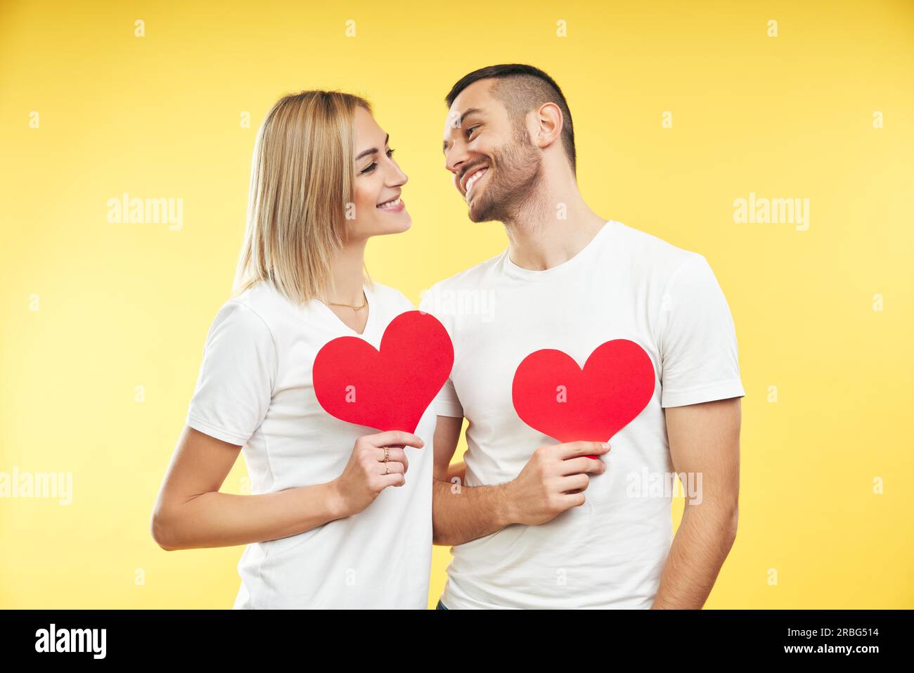 Young couple in love holding big paper hearts in hands over studio ...