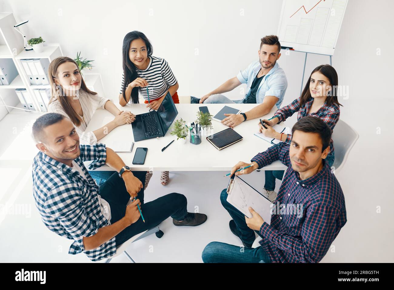 Smiling diverse group of young people working and communicating together in creative office ...