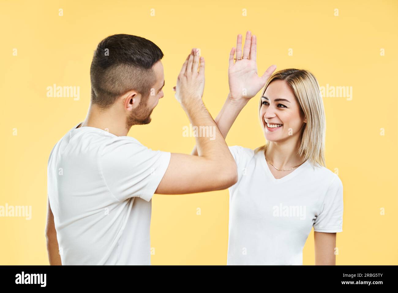 Young smiling couple giving high five to each other over yellow studio ...
