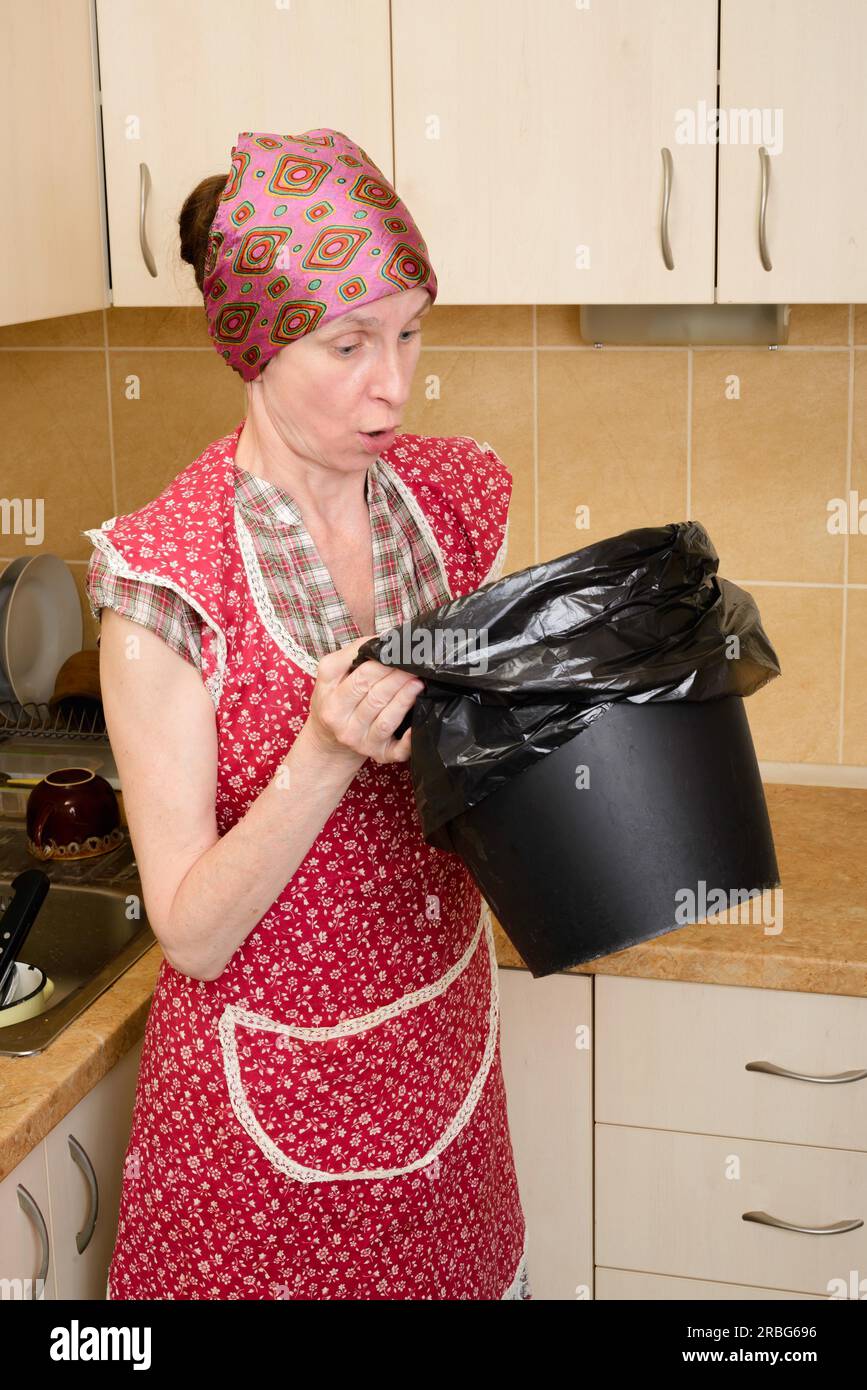 A woman, with a scarf on the head and a red apron, is surprised looking ...