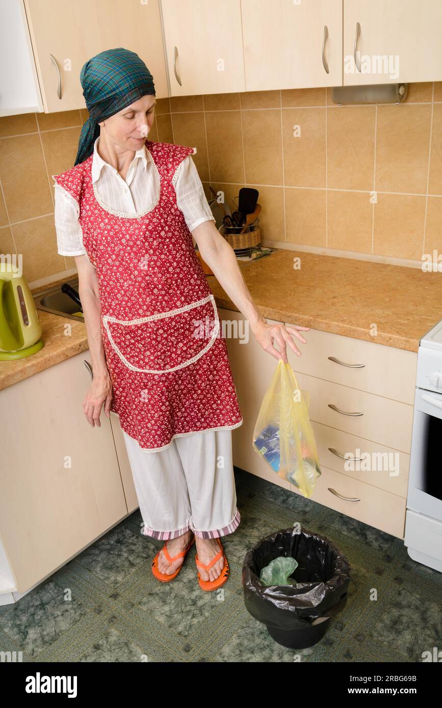 A woman, with a scarf on the head and a red apron, is looking inside a ...