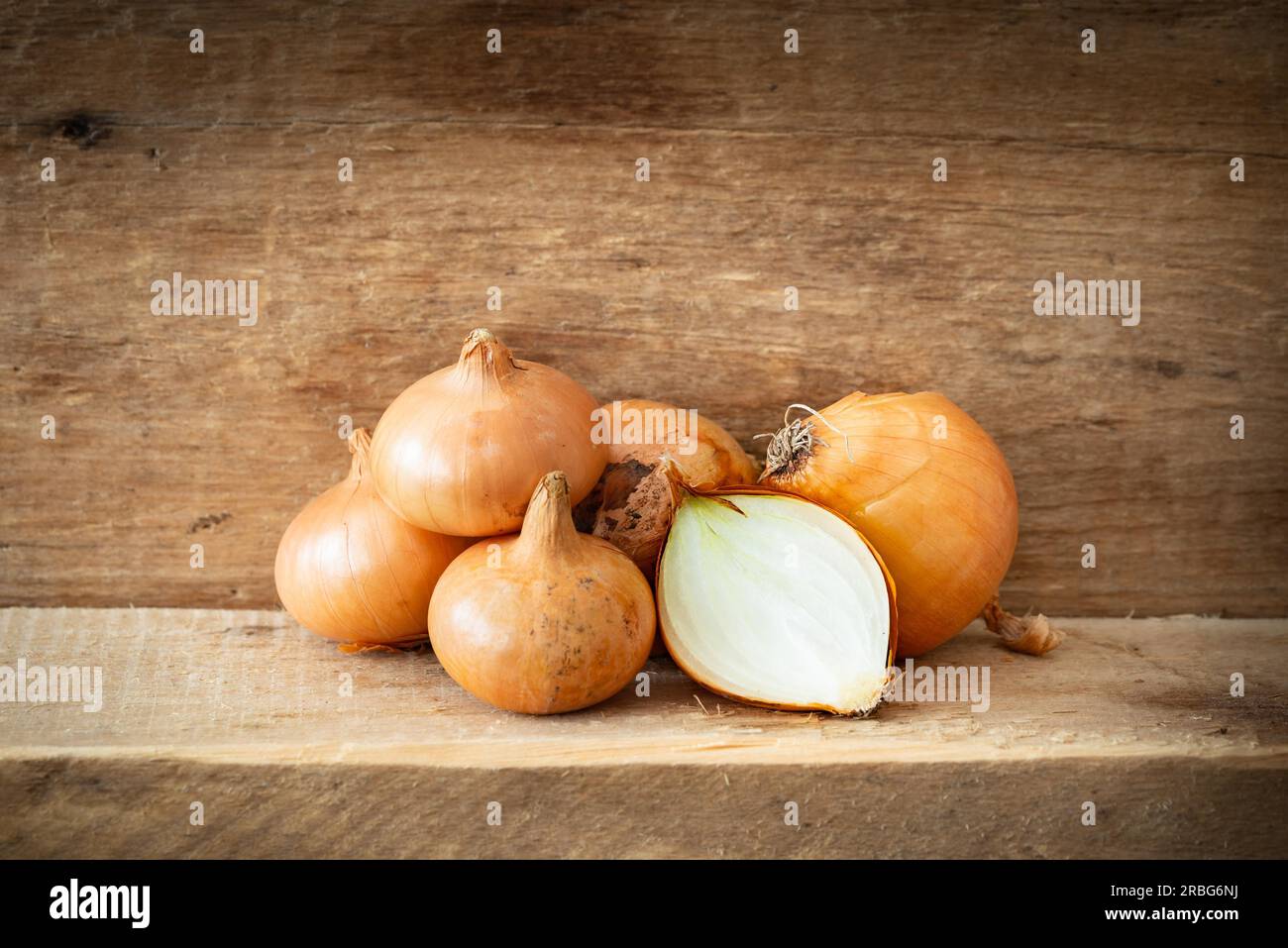 A heap of fresh golden onions on a wooden plank. One onion is cut and ...