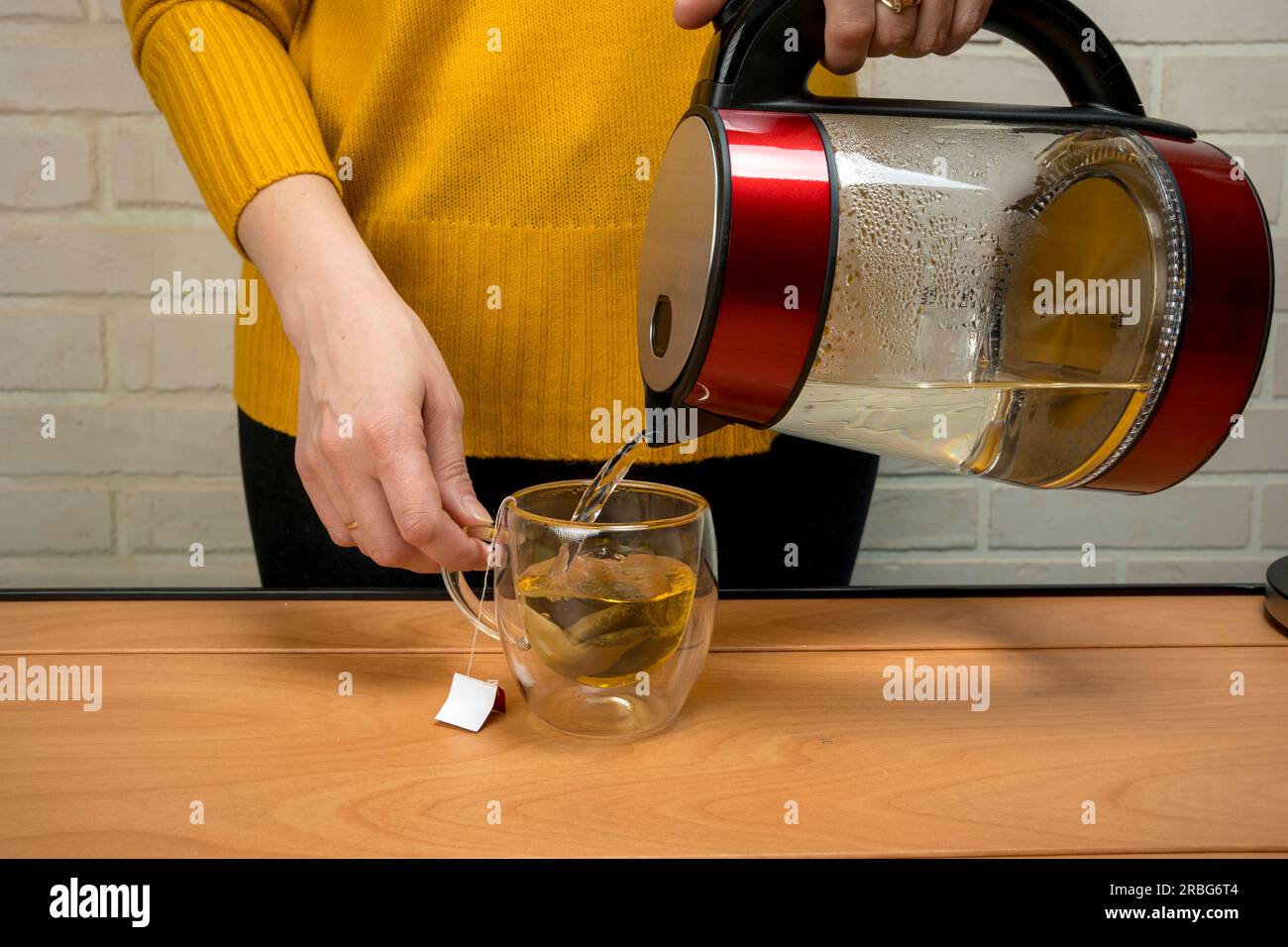 Woman poring hot boiled water from electric kettle into a clear glass ...