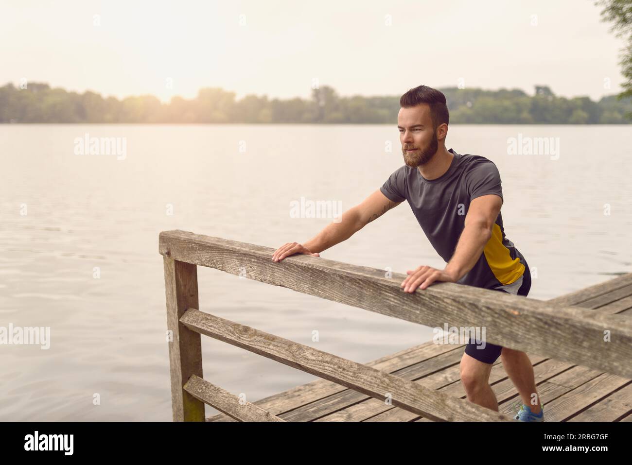 Young man doing stretching exercises on a wooden deck overlooking a ...