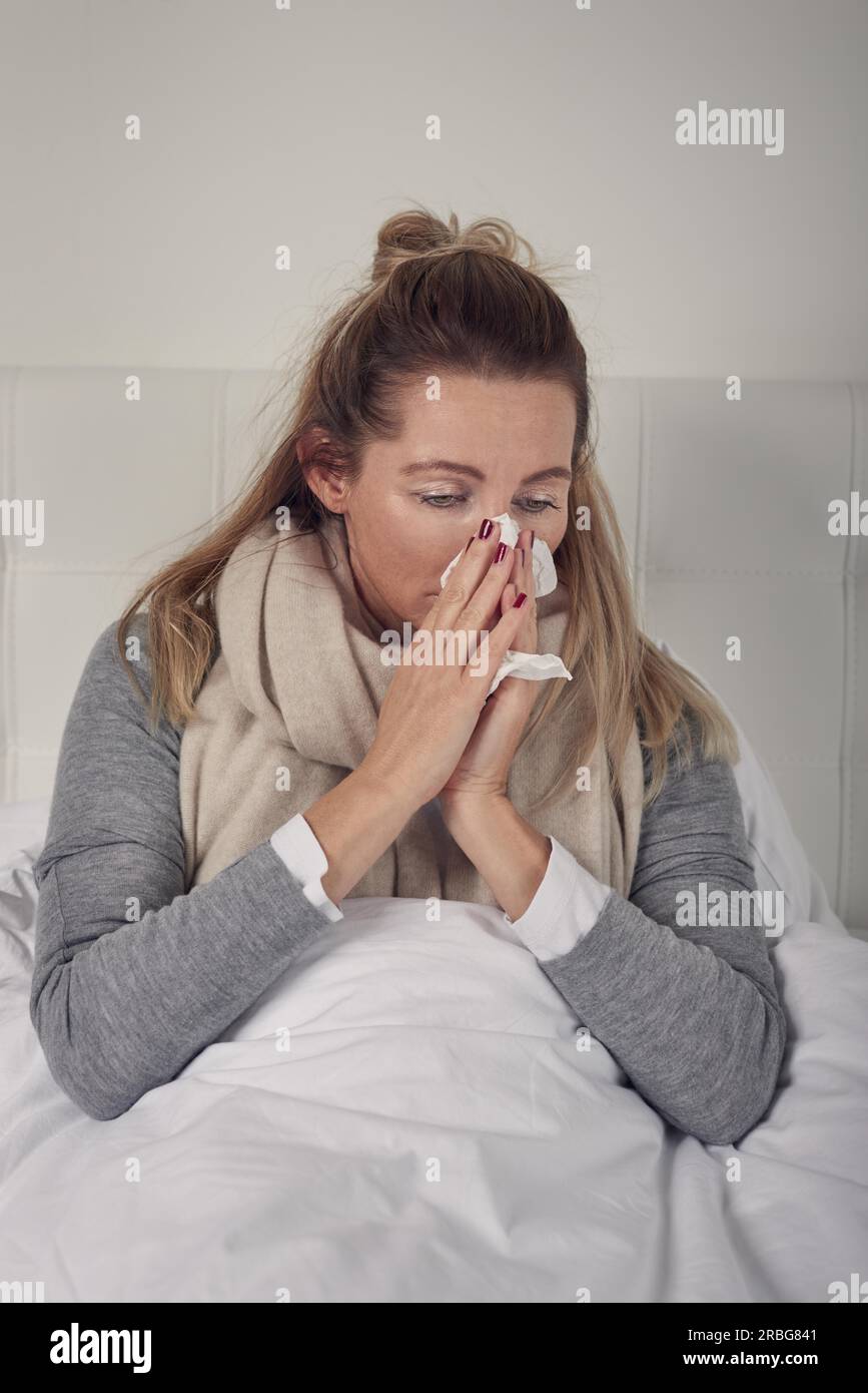 Sick woman with seasonal cold and flu lying wrapped up warmly in bed ...