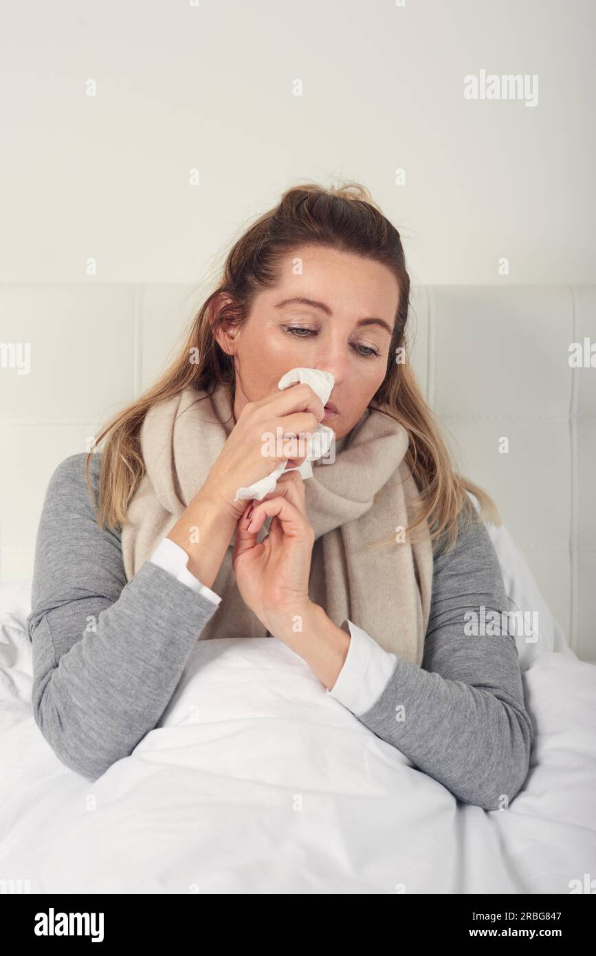 Sick woman with seasonal cold and flu lying wrapped up warmly in bed ...