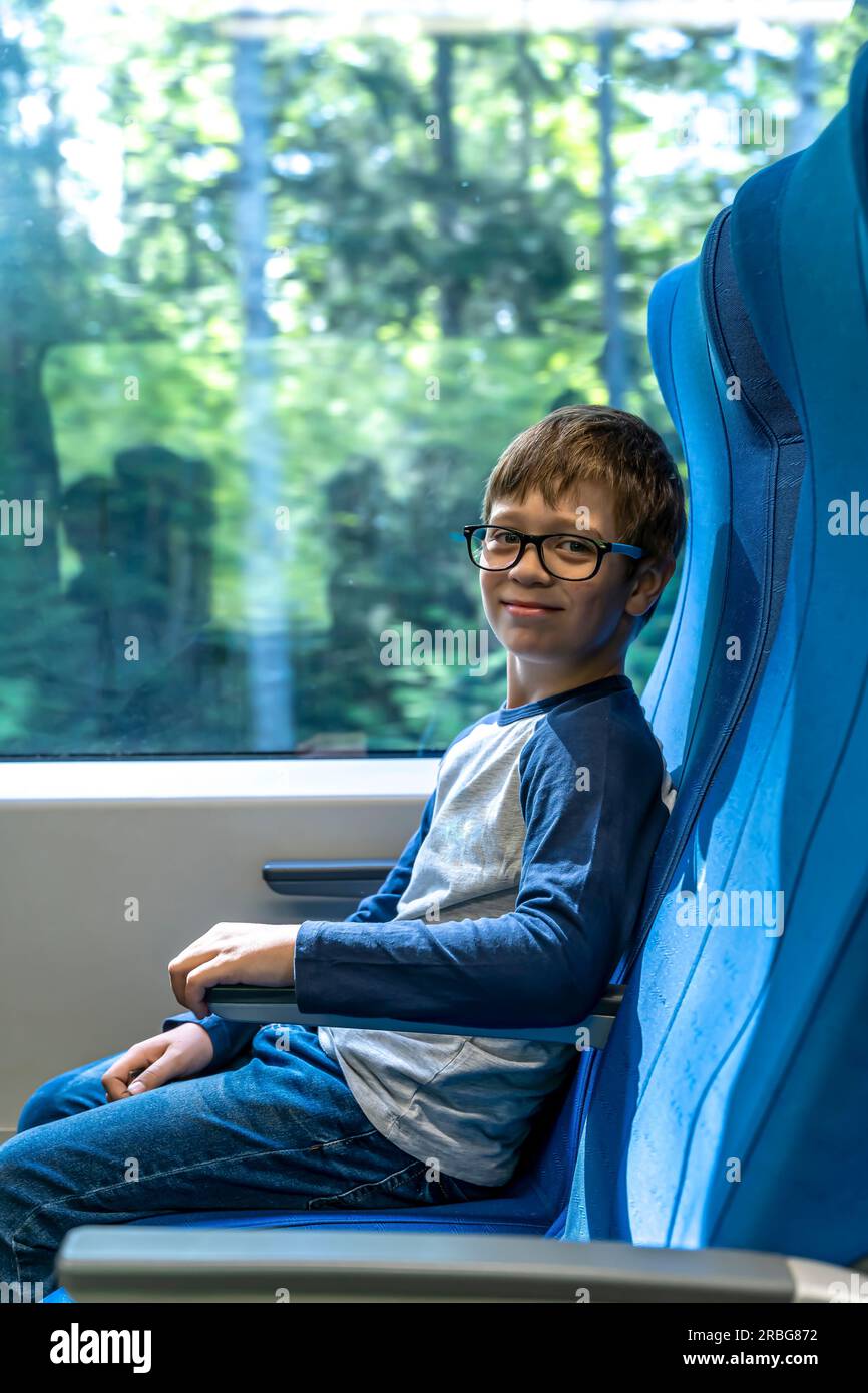 a cute Caucasian school-age boy with glasses rides a commuter train ...