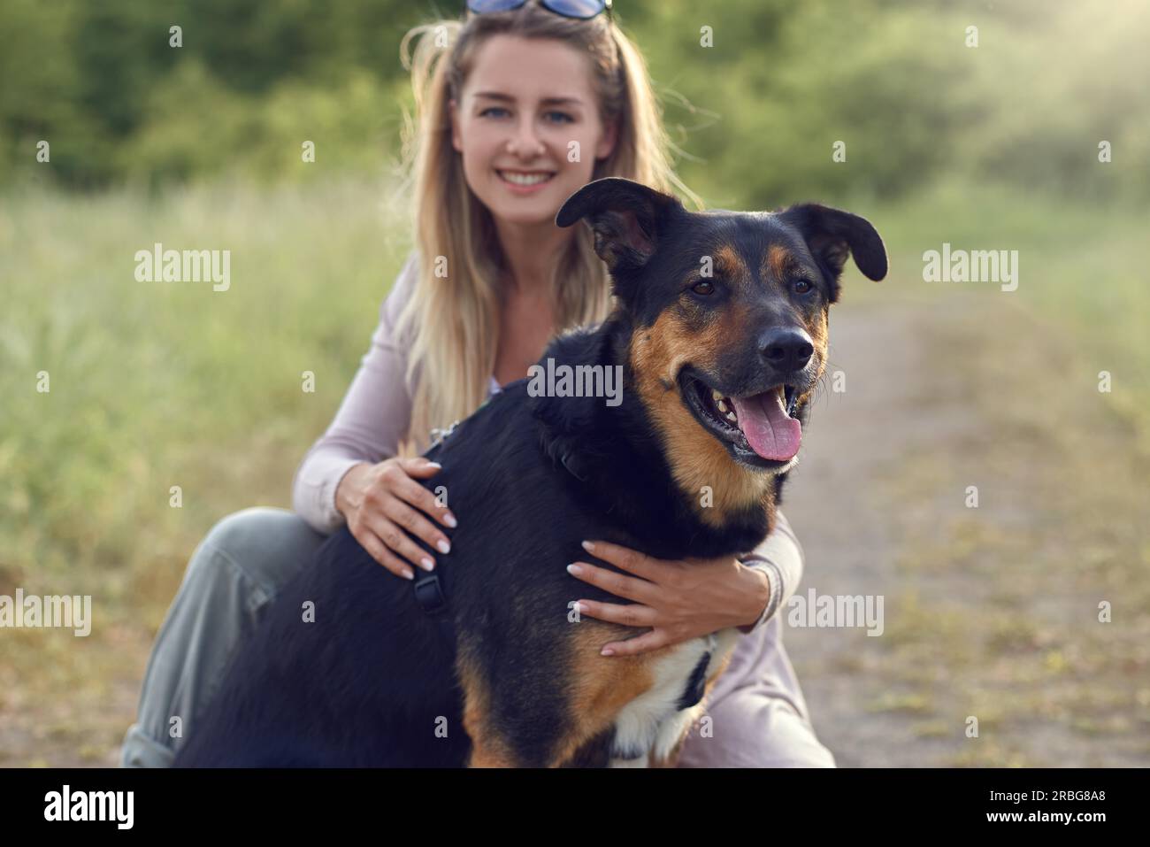 Pretty blond woman with her two dogs crouching with an arm around each ...