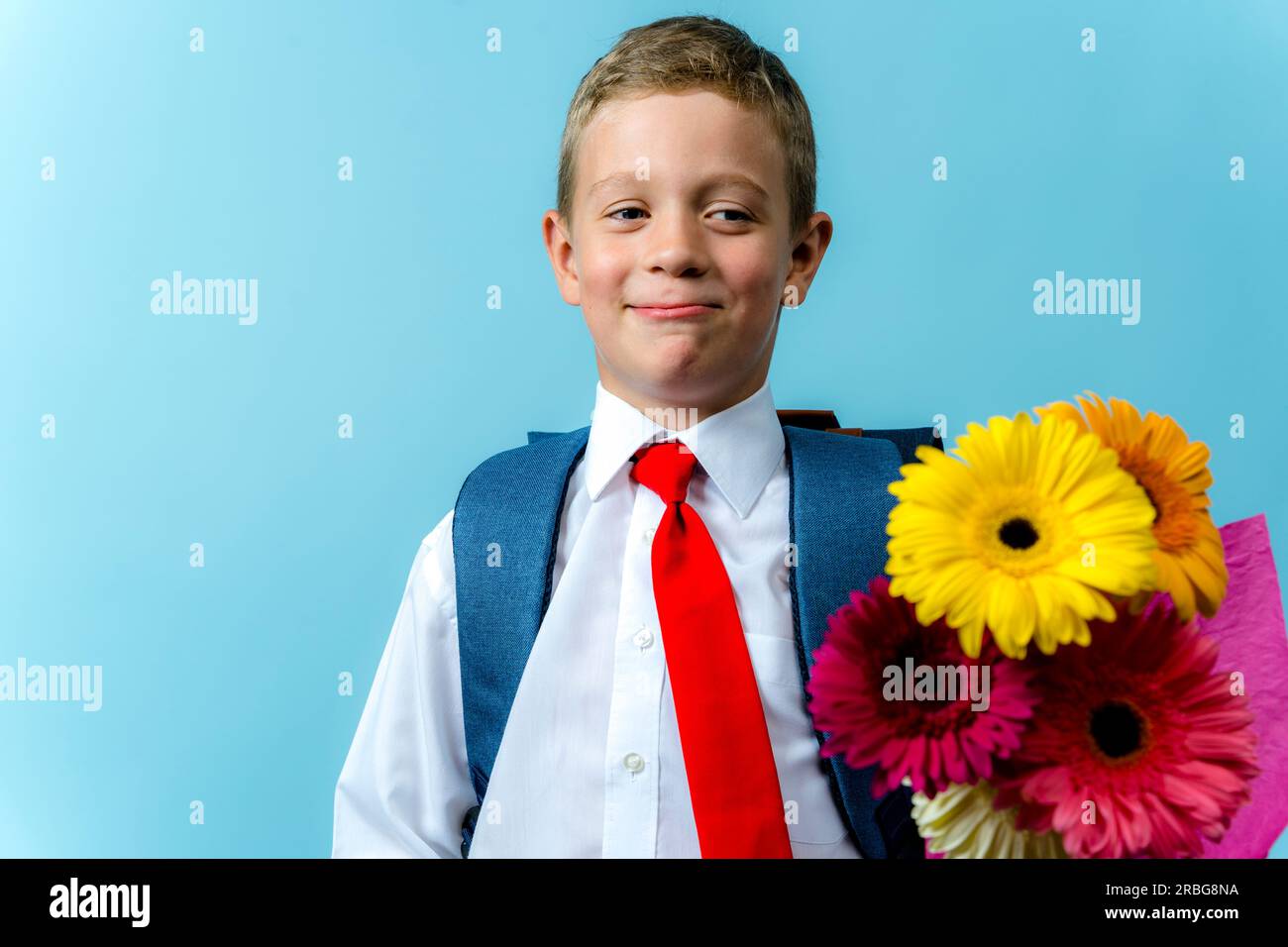 a first grader in a white shirt with a backpack holds a bouquet of ...