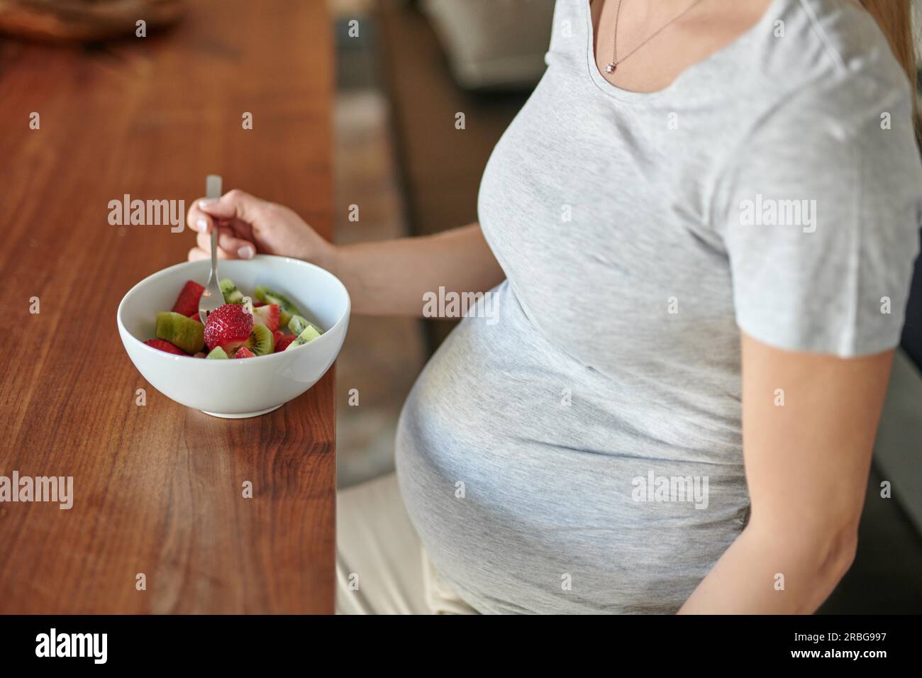 Pregnant woman eating a bowl of fruit salad with fresh strawberries ...