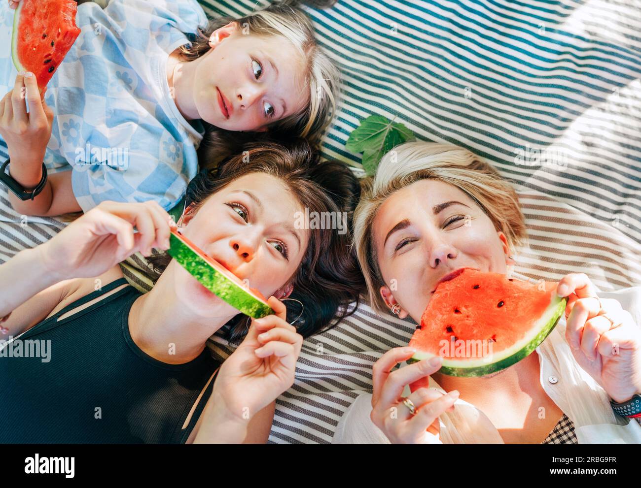 Mother lying with daughters lying on picnic blanket in city park during ...