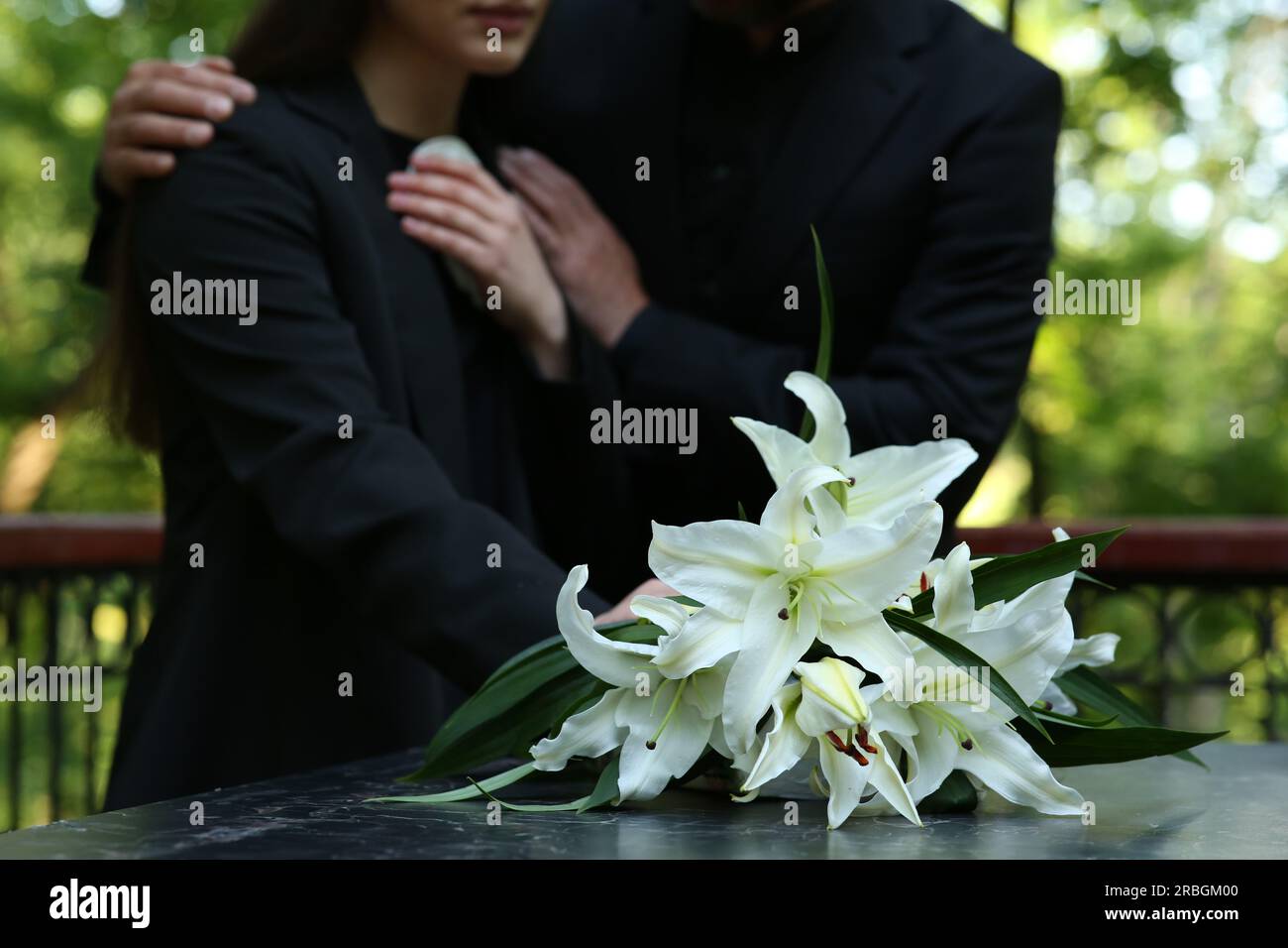 People near white lilies on tombstone at cemetery, closeup. Funeral ...