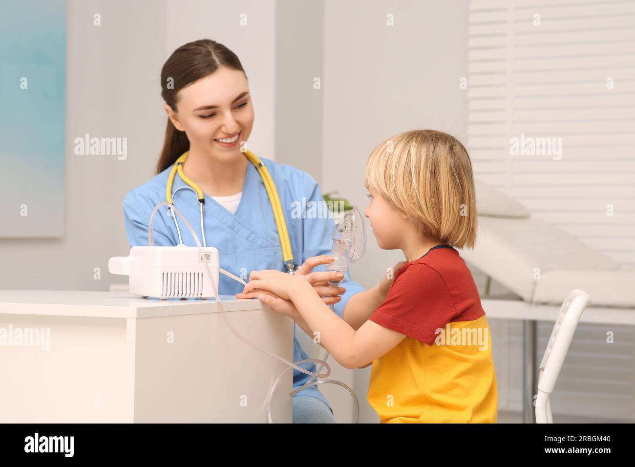 Medical assistant helping sick little boy with nebulizer inhalation at ...