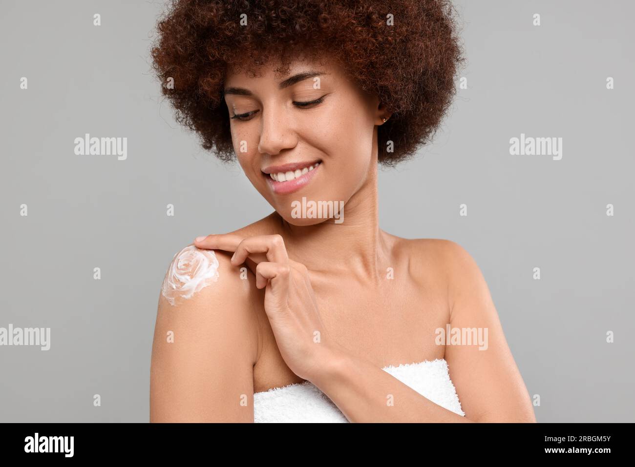 Beautiful young woman applying body cream onto shoulder on grey ...