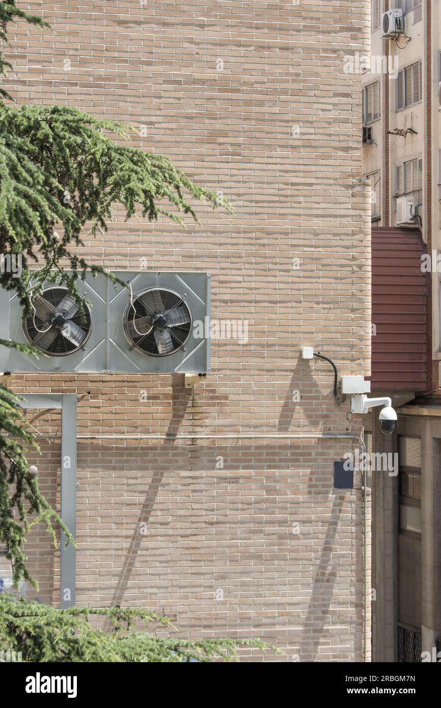 Surveillance camera and air conditioning fans on a wall of a clay brick ...
