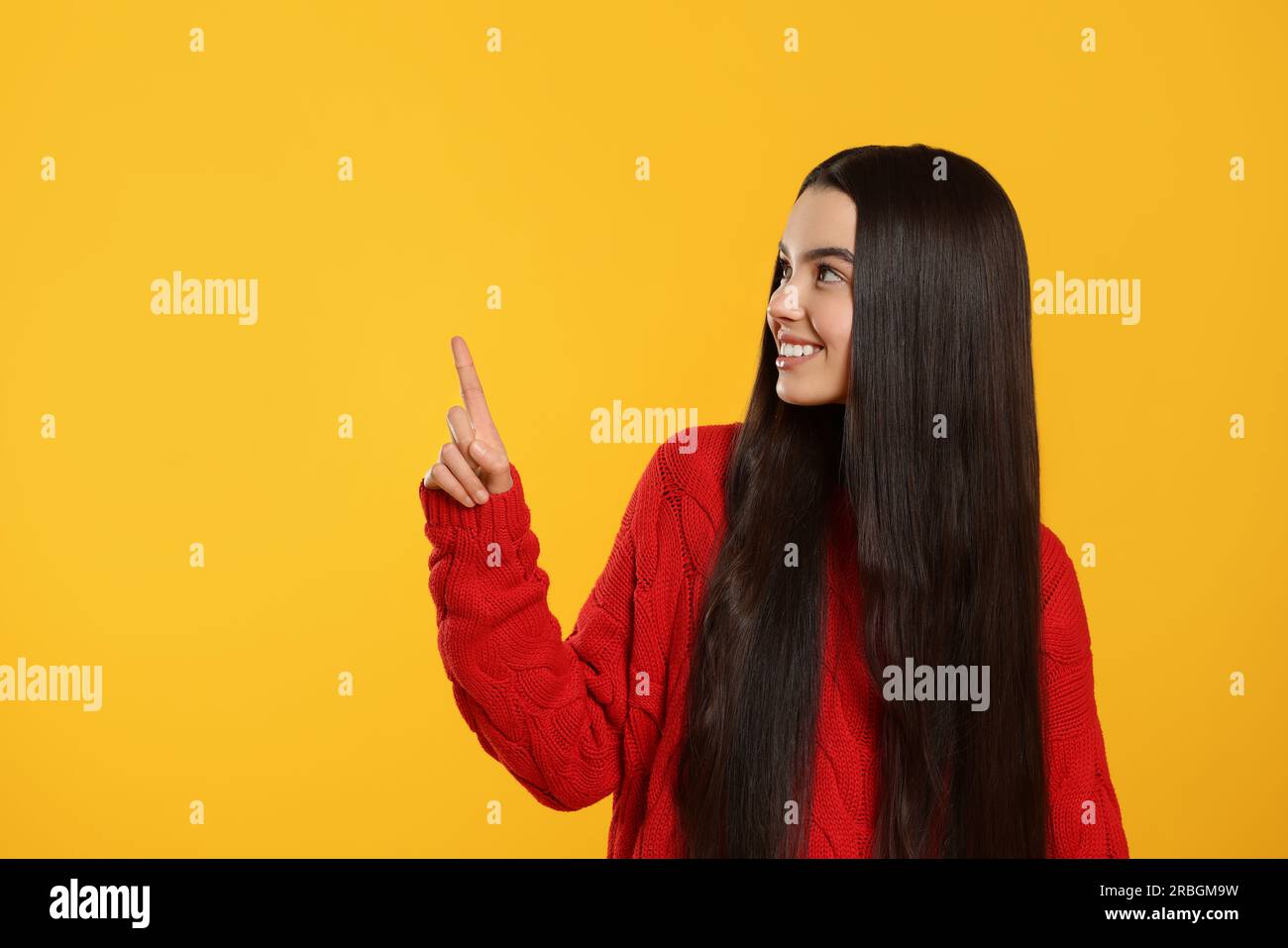 Teenage girl pointing at something on yellow background. Space for text ...