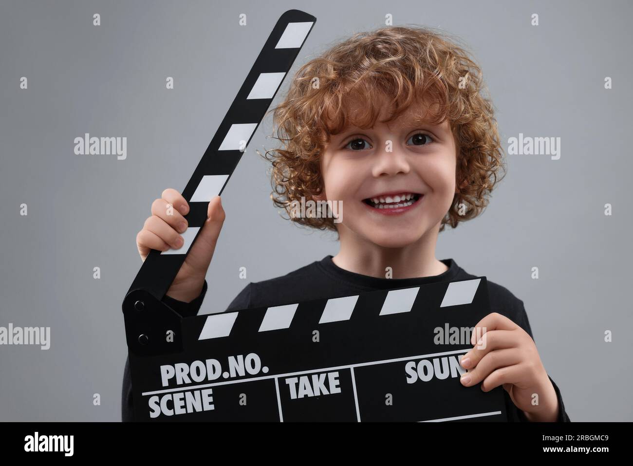 Smiling cute boy with clapperboard on grey background. Little actor ...