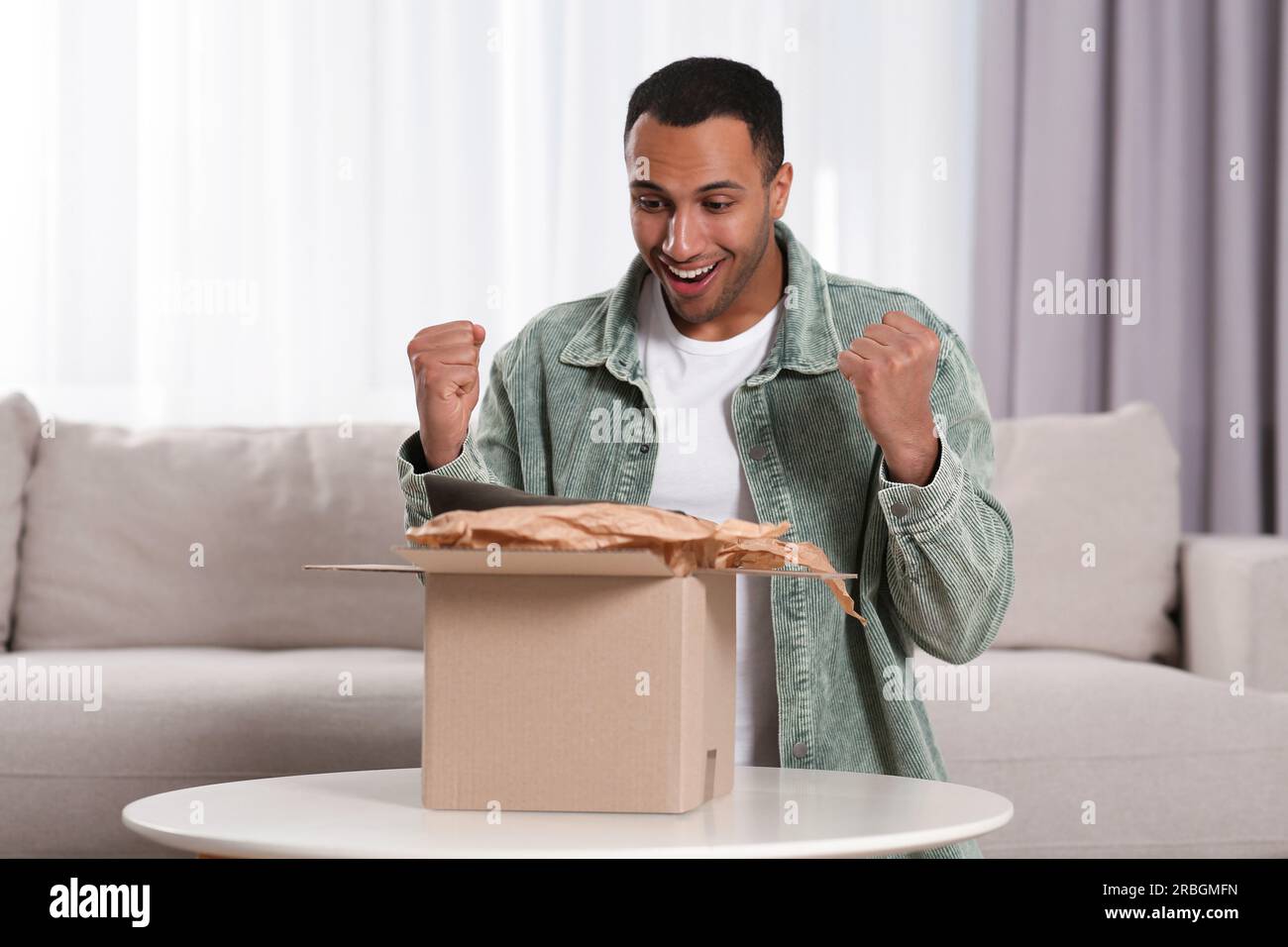 Emotional young man opening parcel at table indoors. Internet shopping ...