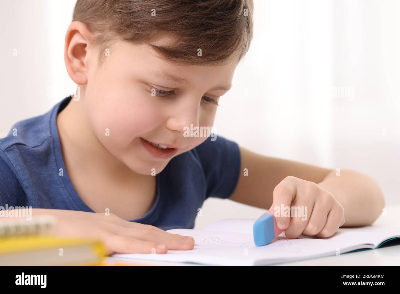 Little boy erasing mistake in his notebook at white desk indoors Stock ...