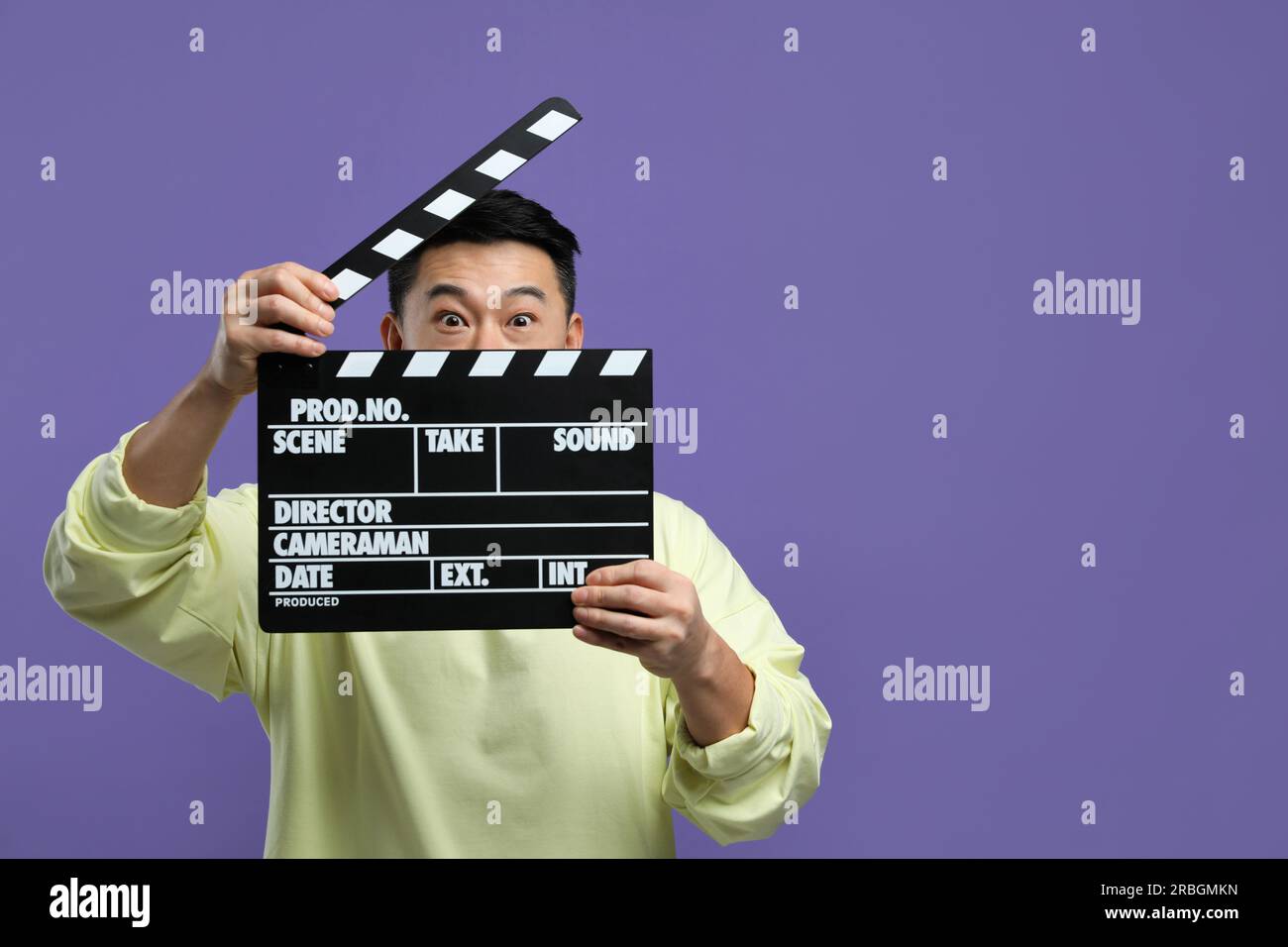 Emotional asian actor with clapperboard on purple background, space for ...