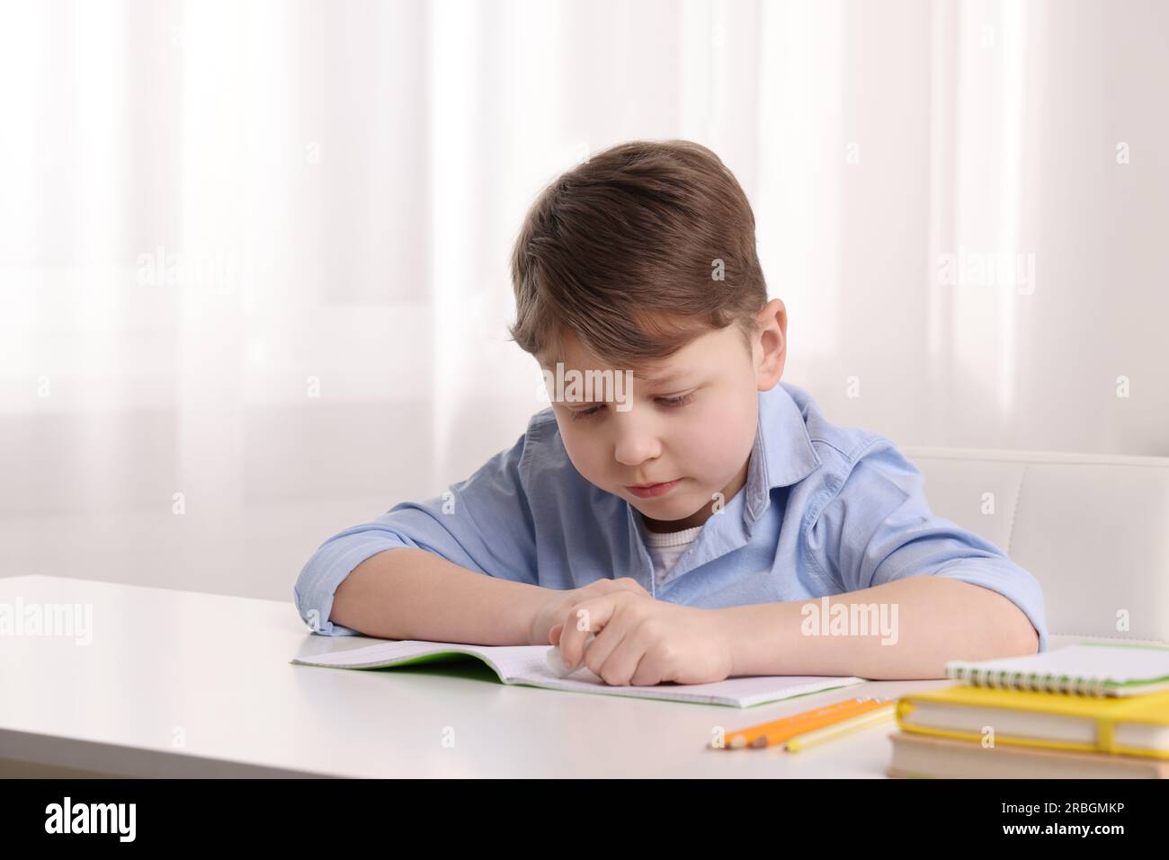 Little boy erasing mistake in his notebook at white desk indoors Stock ...