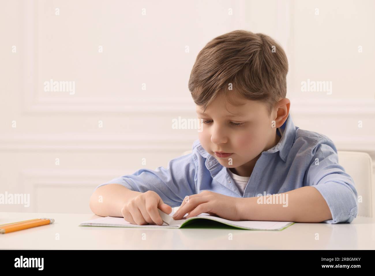 Little boy erasing mistake in his notebook at white desk indoors Stock ...