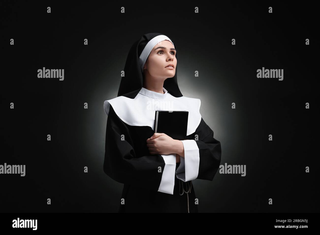 Young nun with Bible on black background Stock Photo - Alamy