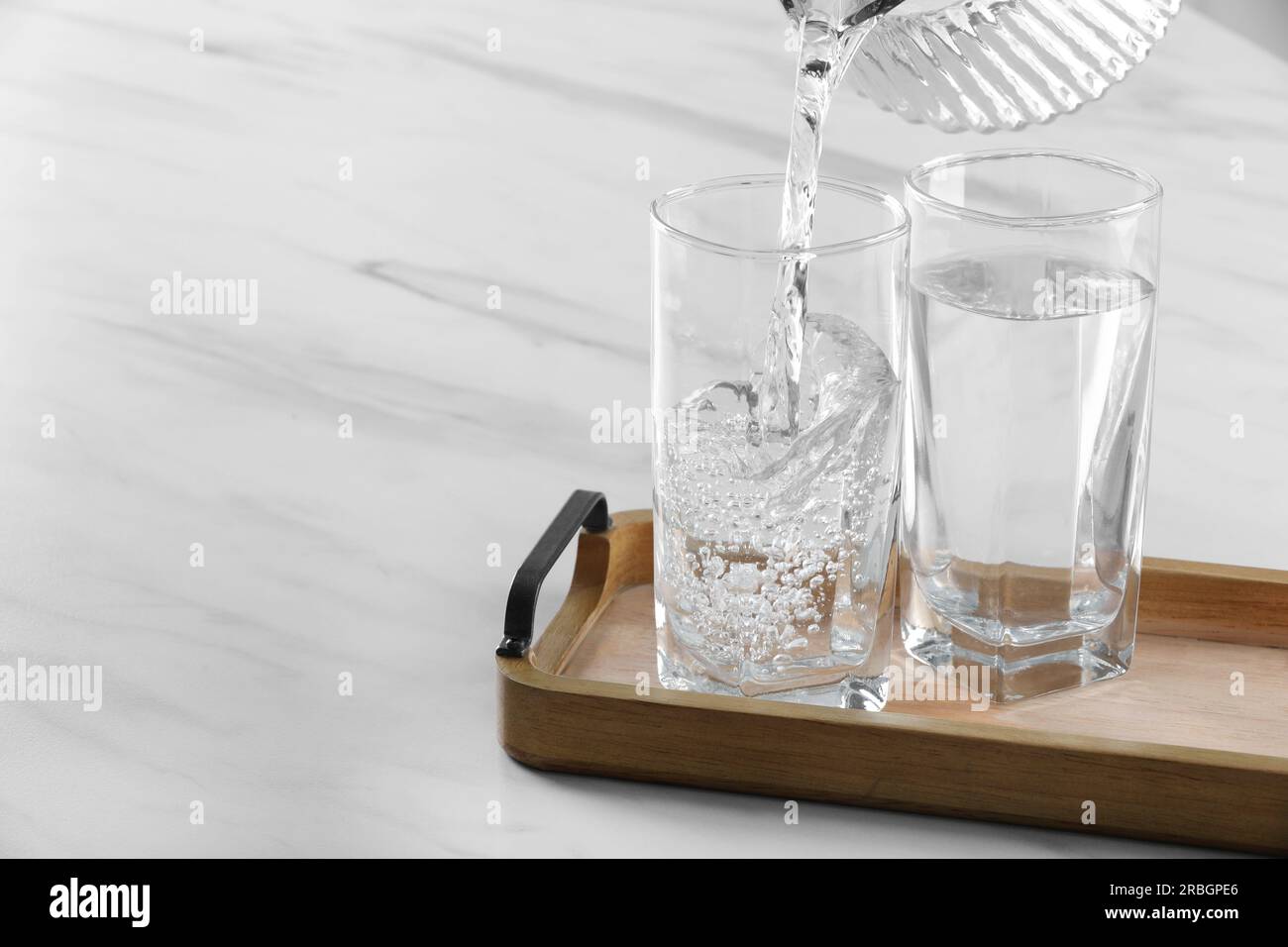 Pouring water from jug into glass at white marble table. Space for text ...