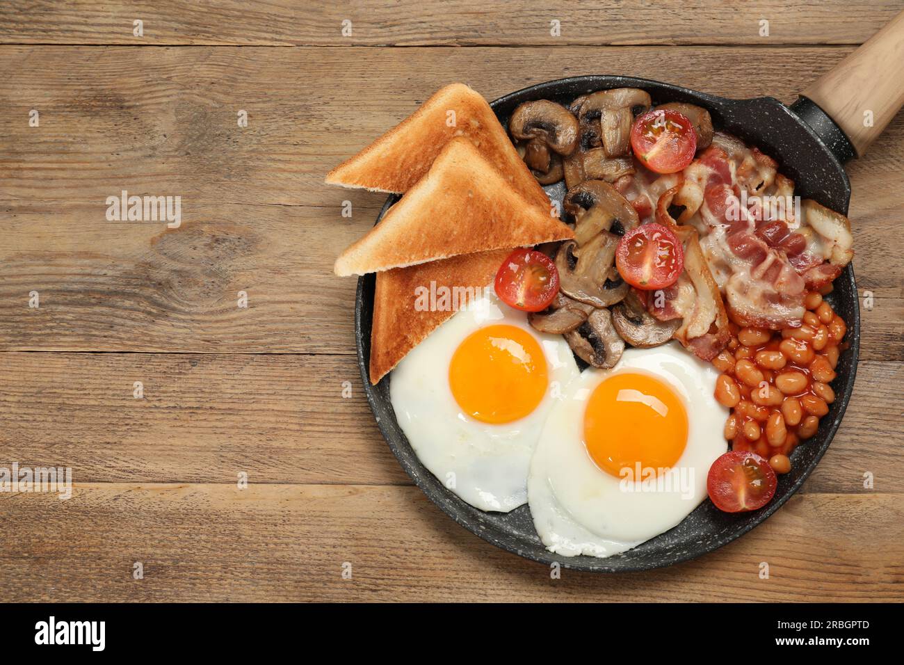Serving pan of fried eggs, mushrooms, beans, bacon, tomatoes and ...