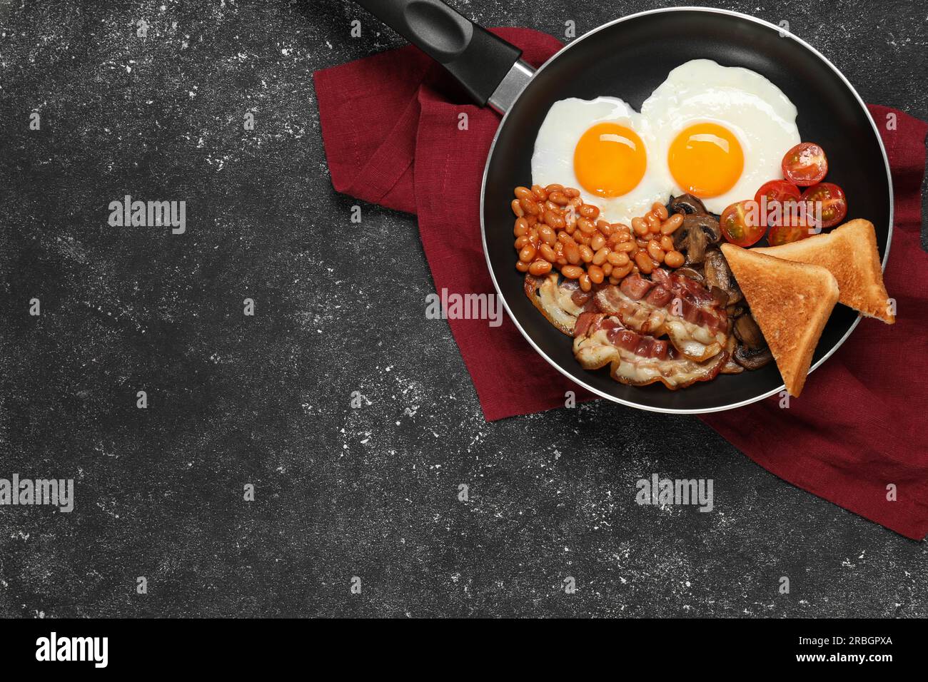 Frying pan with cooked traditional English breakfast on black textured ...