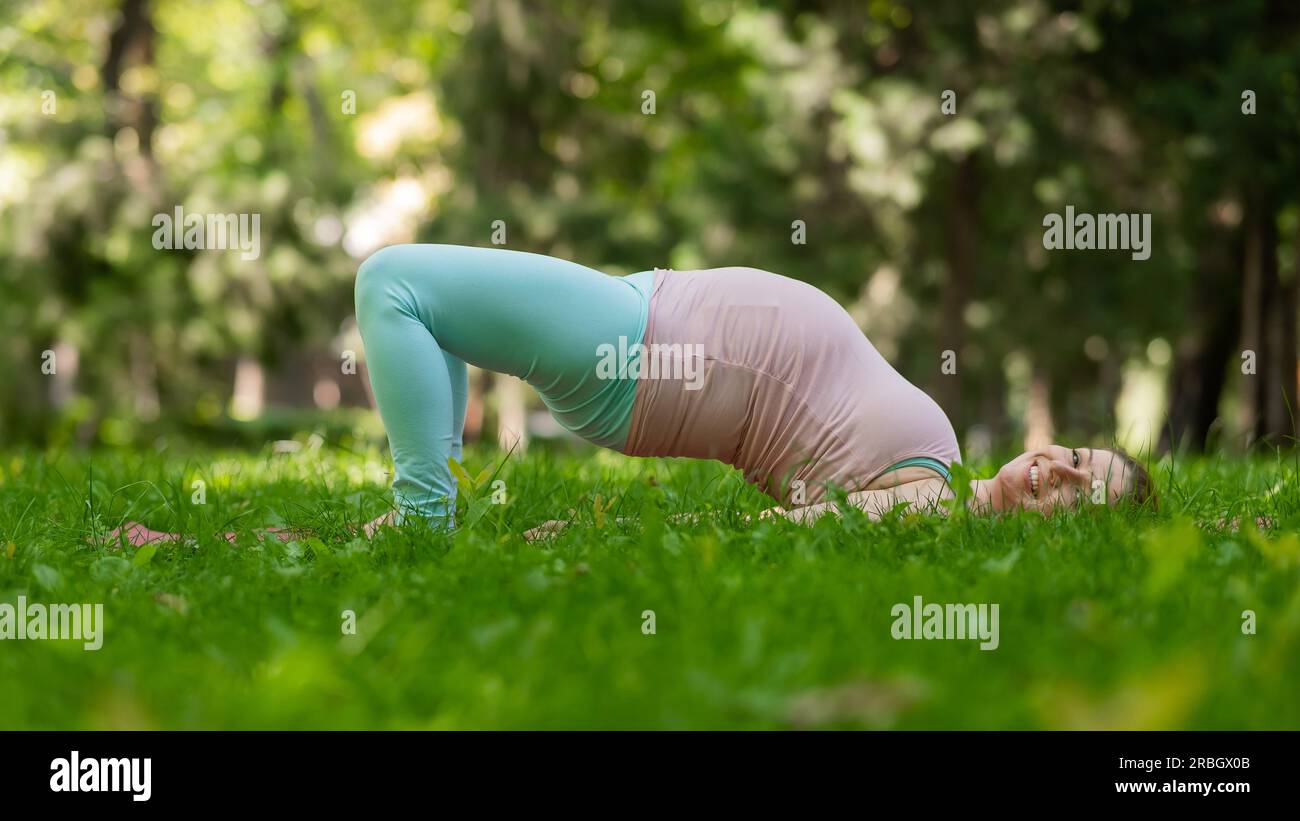 Pregnant caucasian woman doing yoga in the park. Prenatal shoulder ...