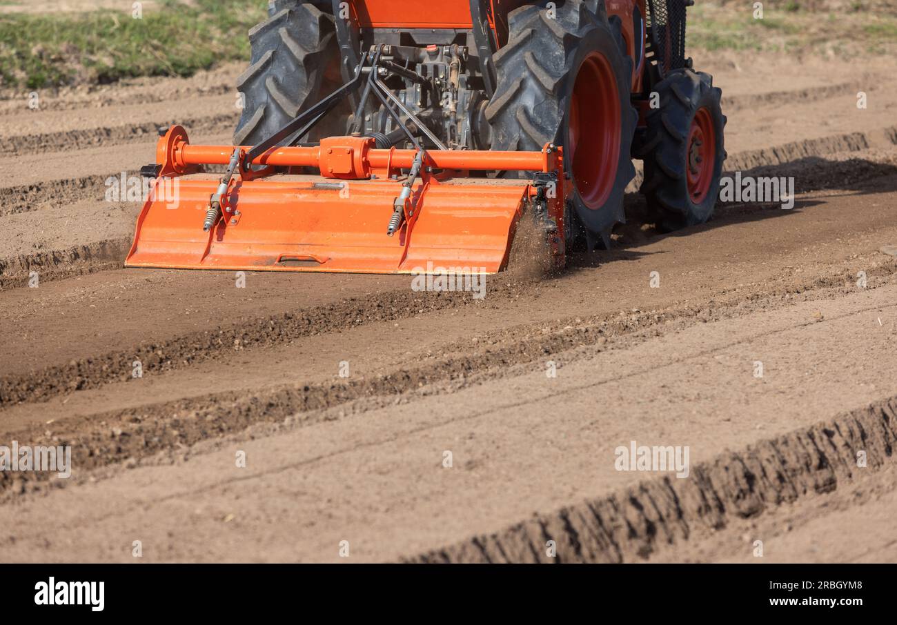 Tractor cultivating land with a rotary tiller in farm Stock Photo - Alamy