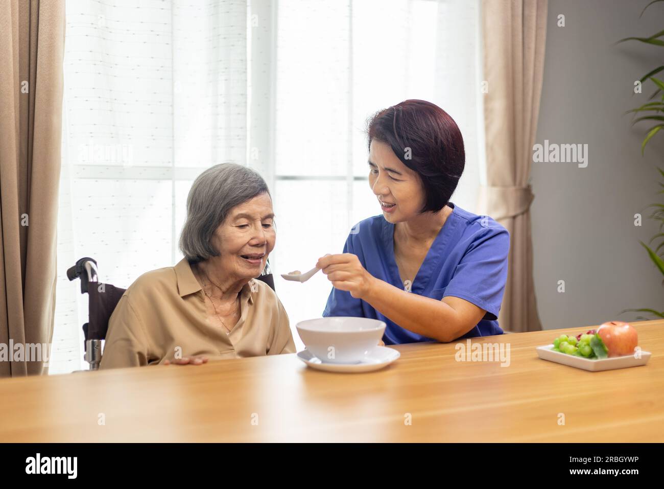 Caregiver feeding elderly asian woman with soup Stock Photo - Alamy