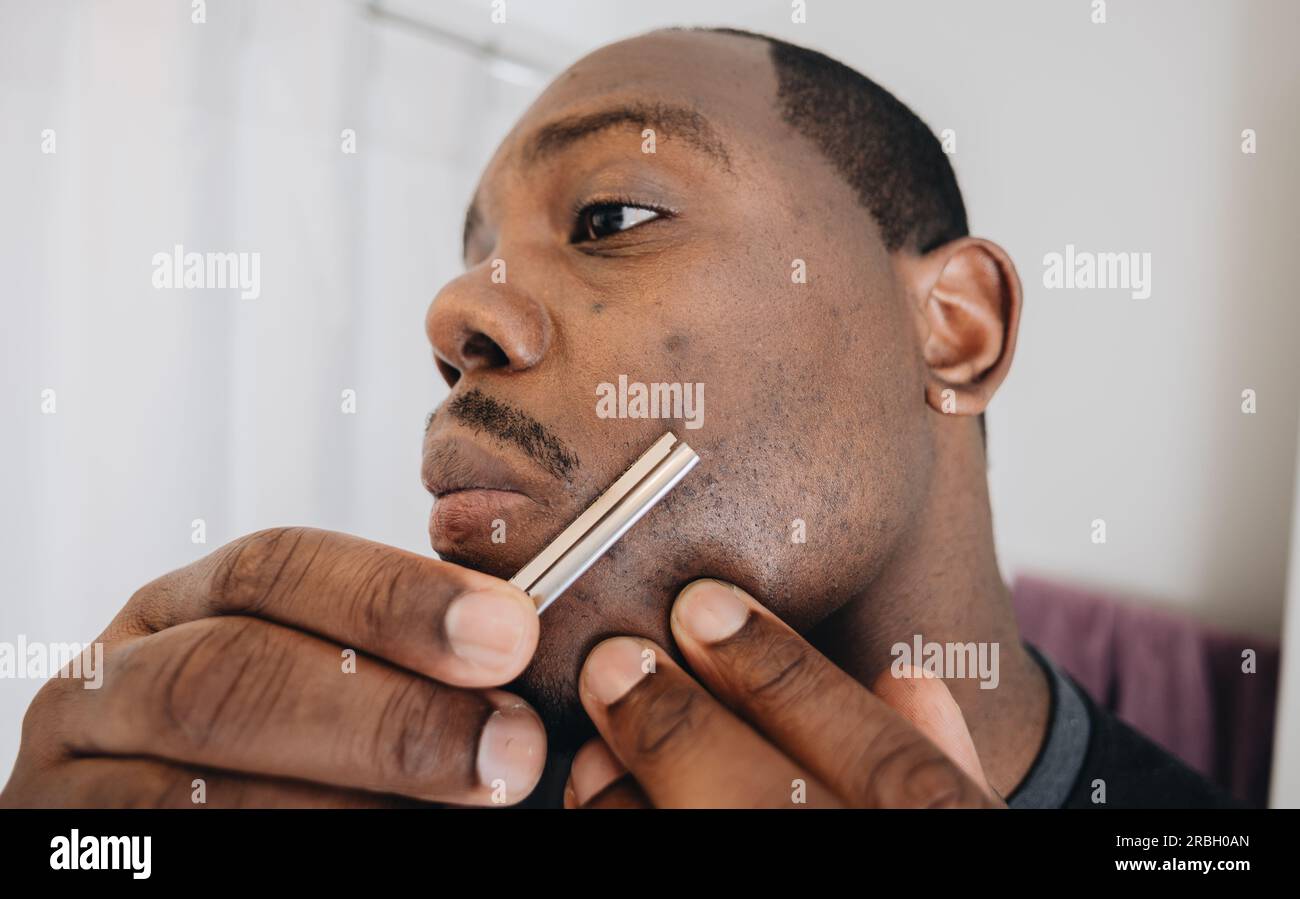African American man in bathroom at home shaving with razor blade after ...