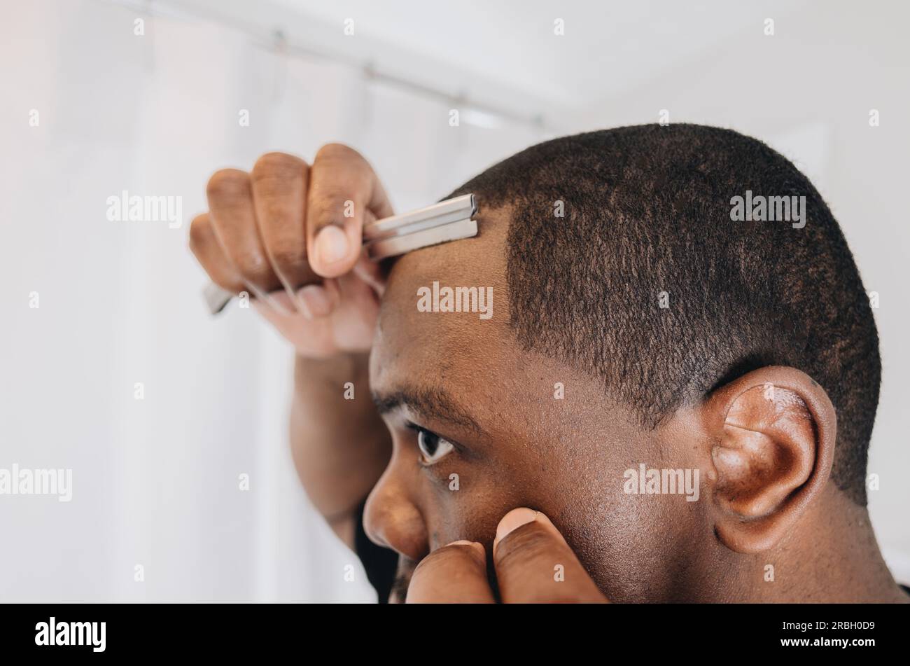 African American man in bathroom at home shaving with razor blade after ...