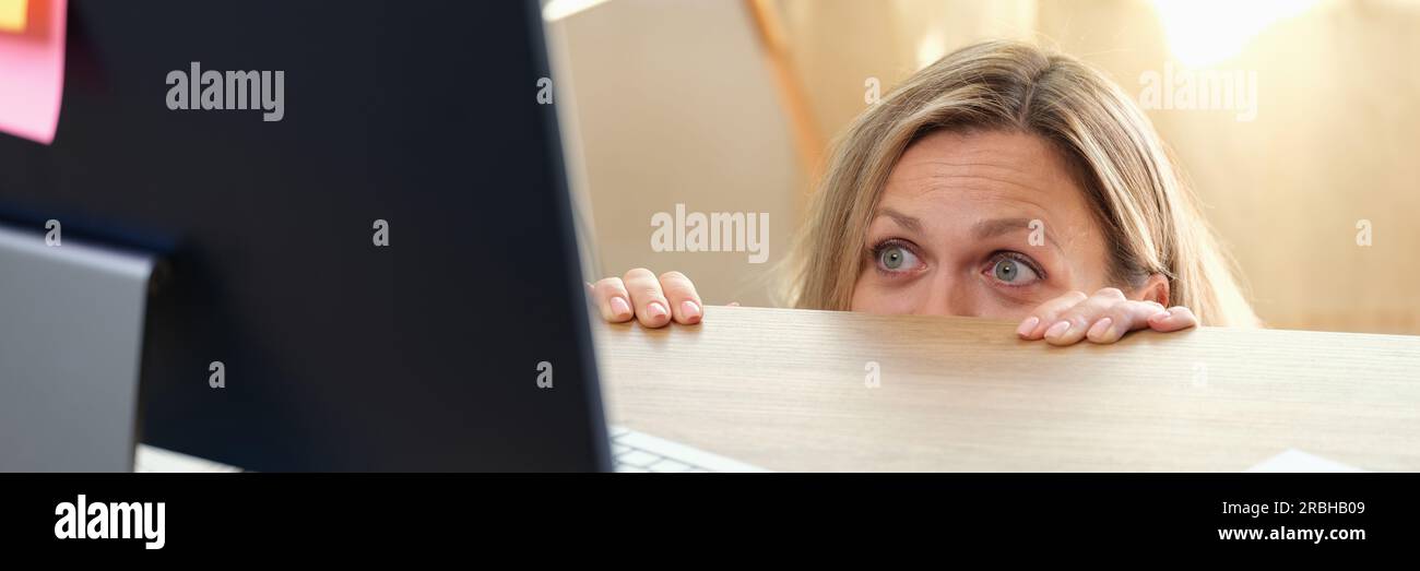 Surprised excited woman peeping out table and looking at pc screen ...