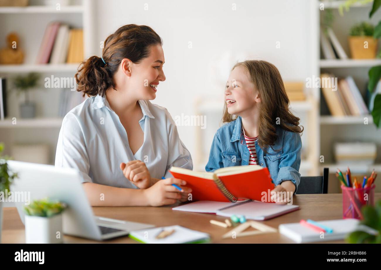Happy child and adult are sitting at desk. Girl doing homework or ...