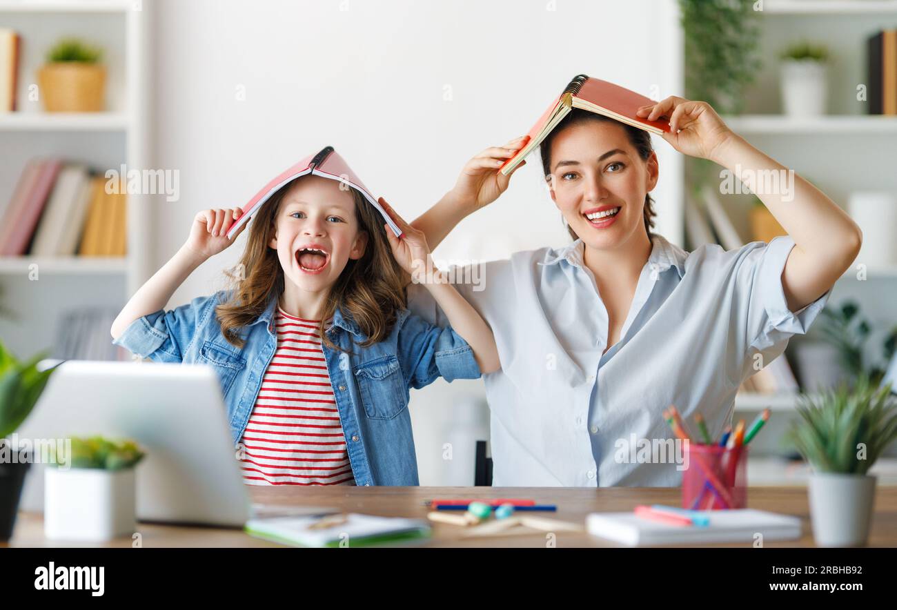 Happy child and adult are sitting at desk. Girl doing homework or ...