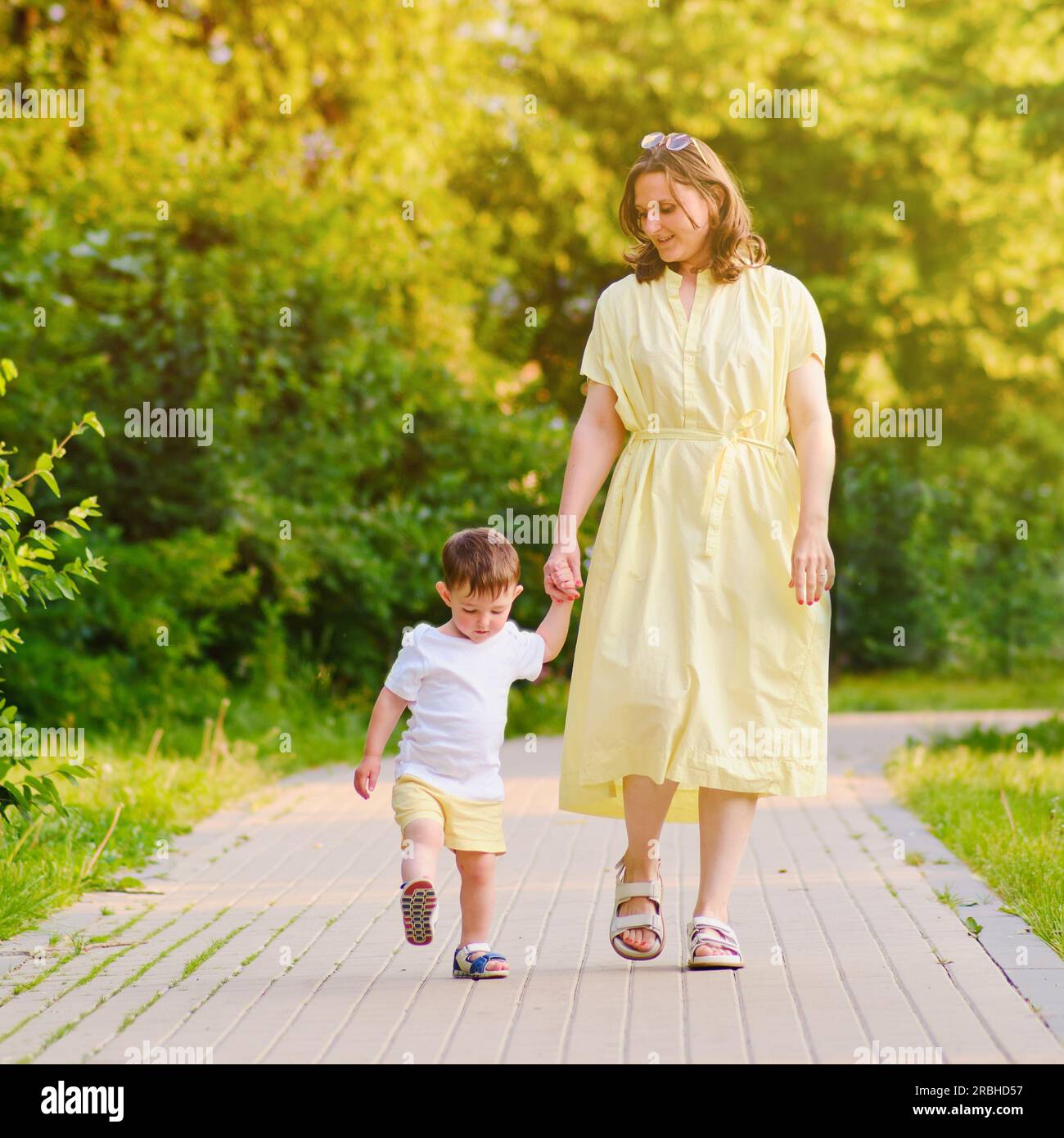 A child takes steps holding a mother woman by the hand along a path in ...