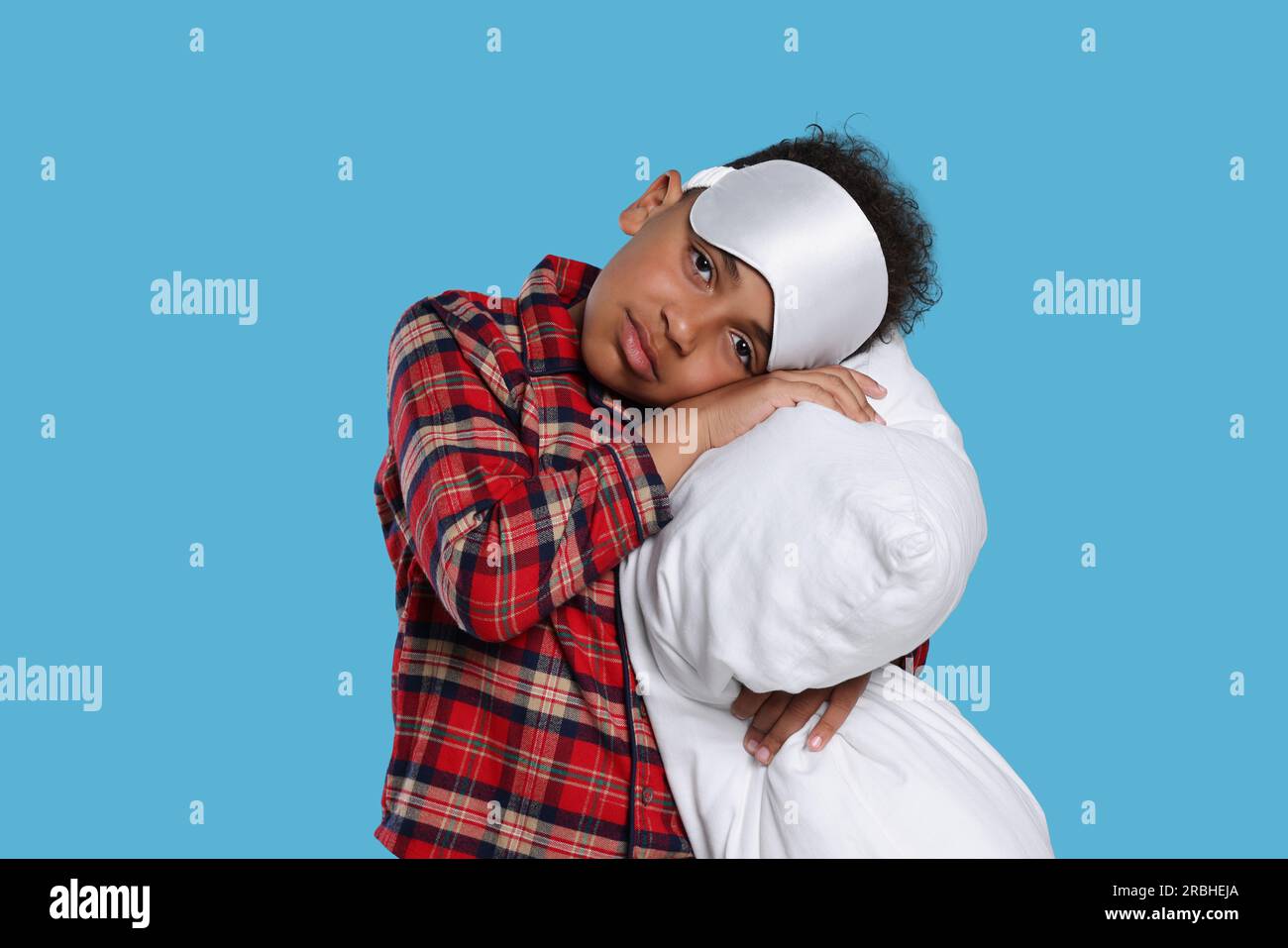 Boy with pillow and sleep mask on light blue background. Insomnia ...