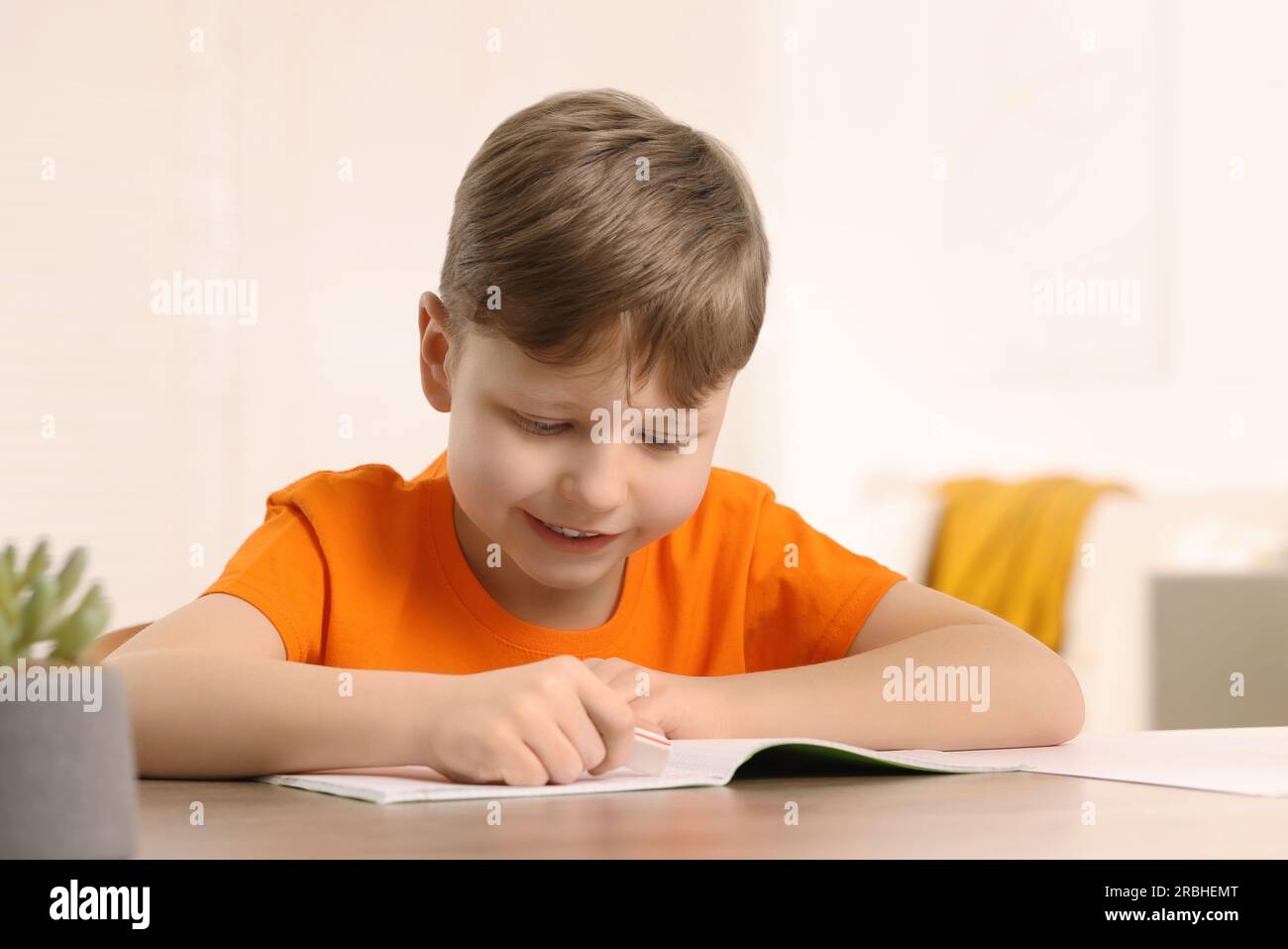 Little boy erasing mistake in his notebook at wooden desk indoors Stock ...