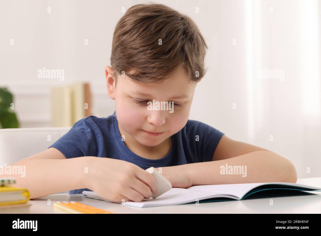 Little boy erasing mistake in his notebook at white desk indoors Stock ...