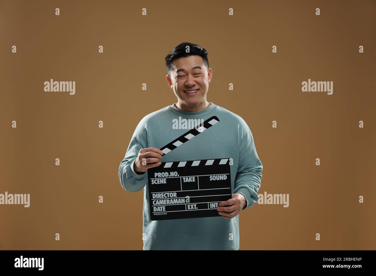 Happy asian actor with clapperboard on brown background. Film industry ...